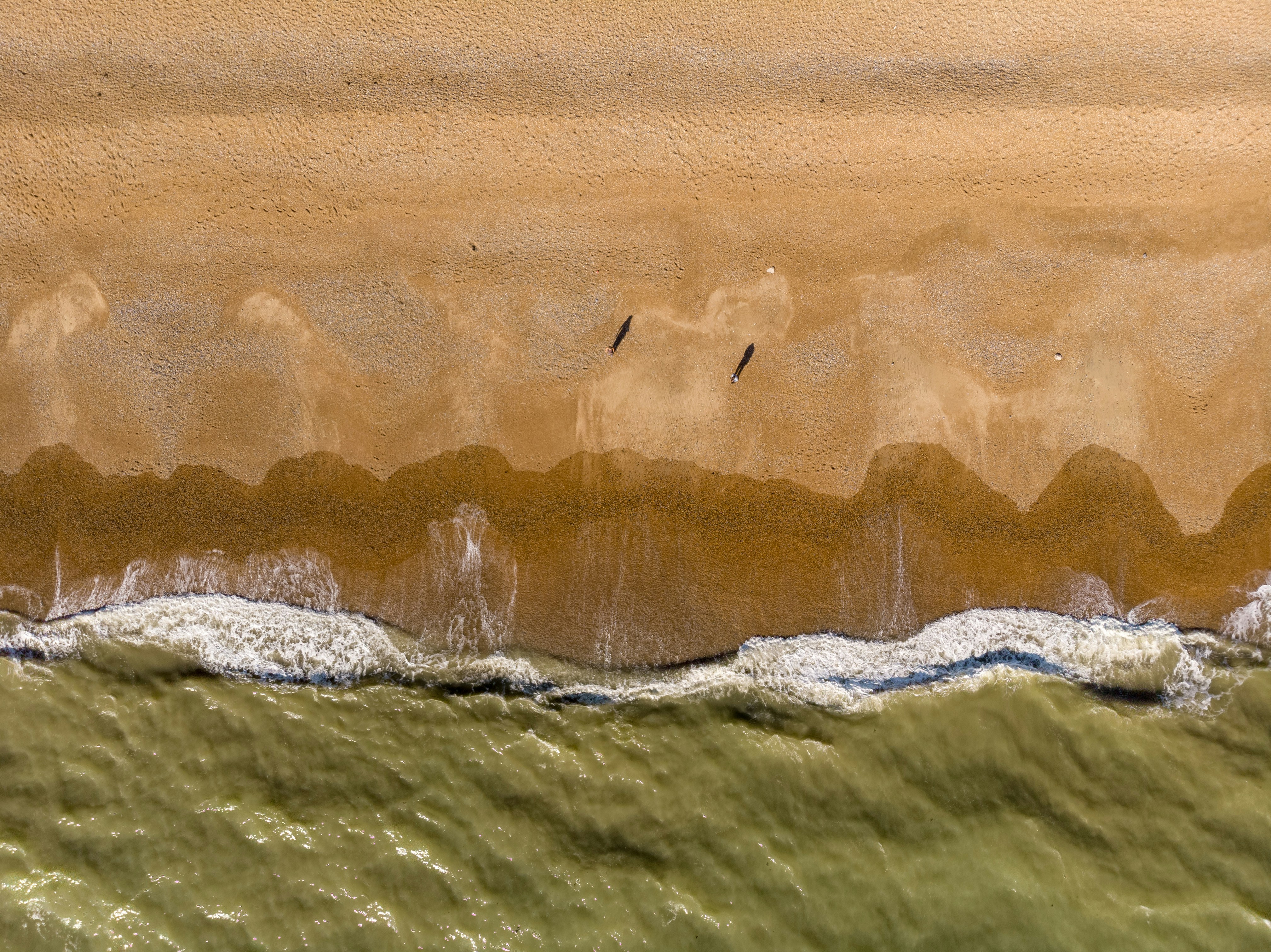 Aerial view showcasing the intricate patterns of sand and waves where the ocean meets the shore, highlighting the dynamic interplay between land and water.