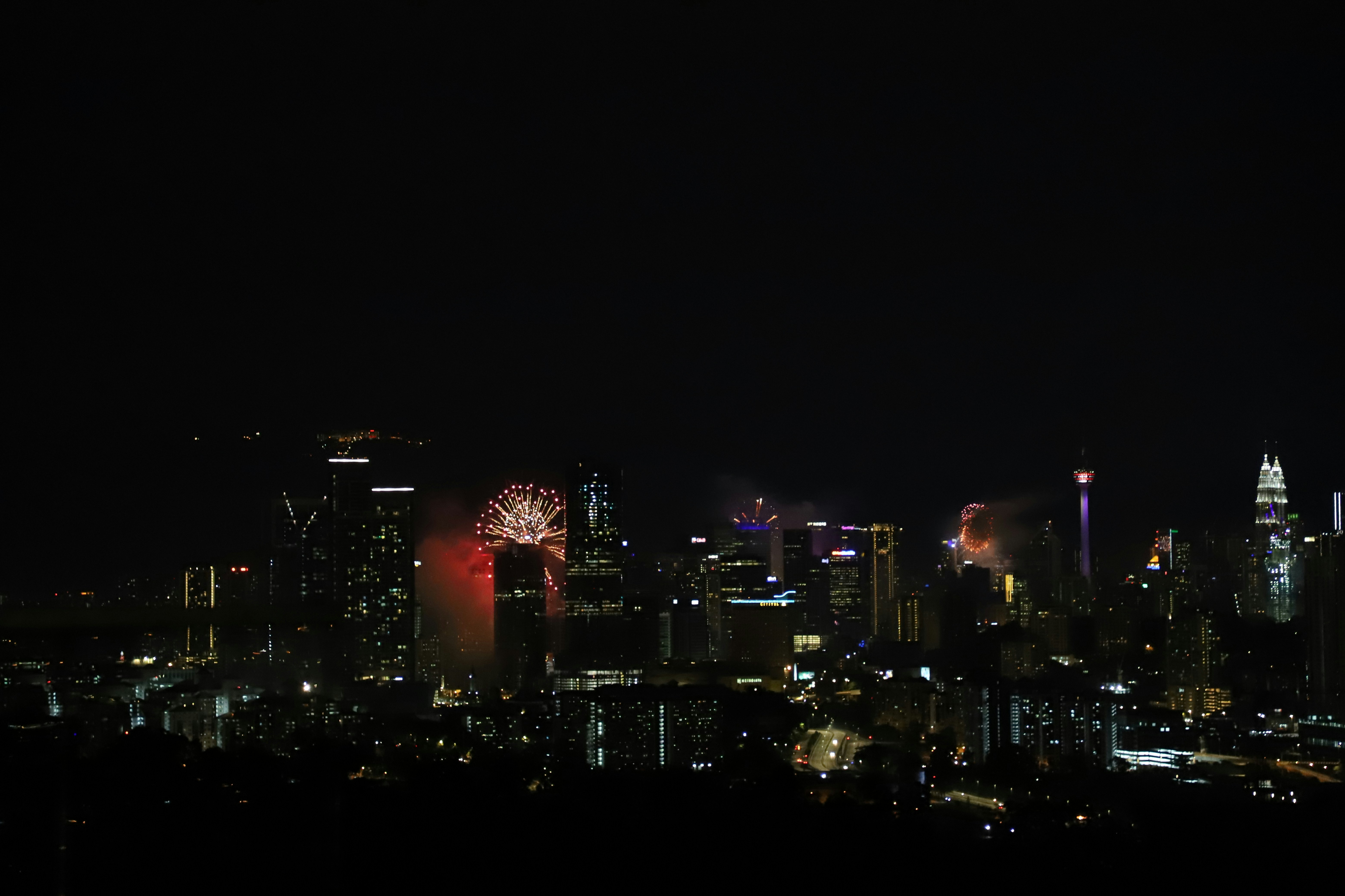 Fireworks illuminate a vibrant city skyline at night, showcasing a blend of modern architecture and festive energy.