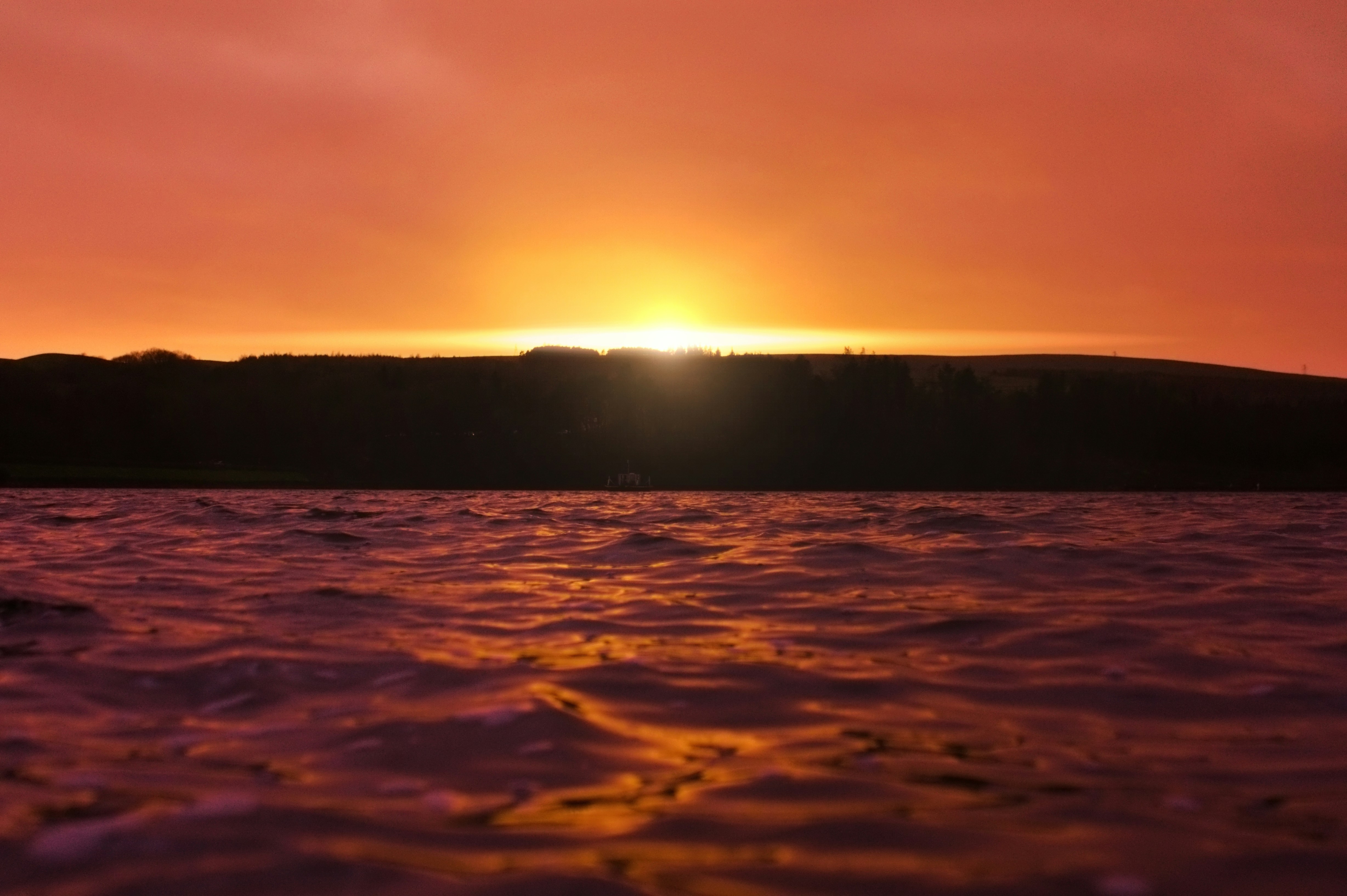 Sunset casting a golden glow over a rippling lake and silhouetted hills.