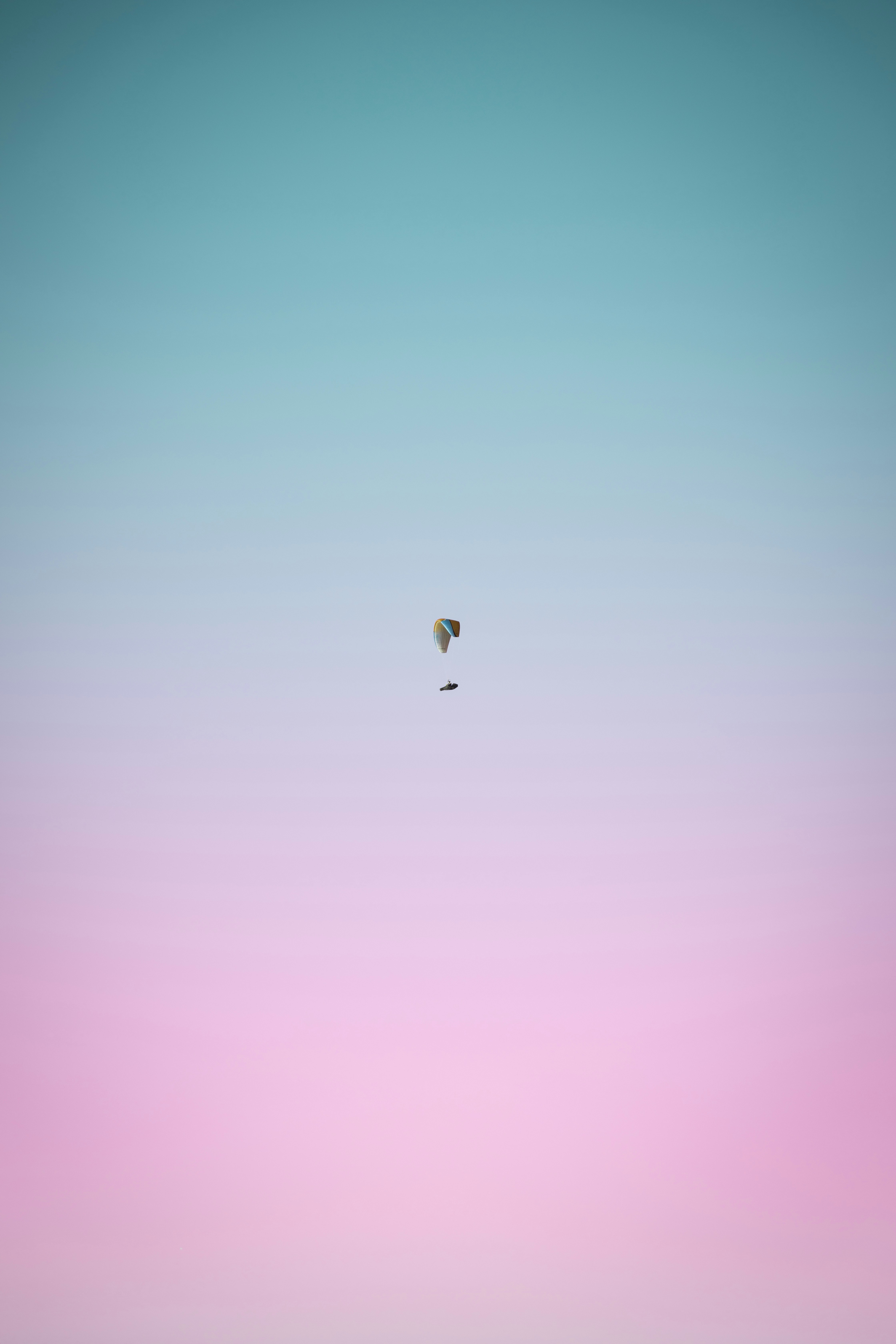 A paraglider gracefully floats against a serene gradient sky transitioning from blue to pink.