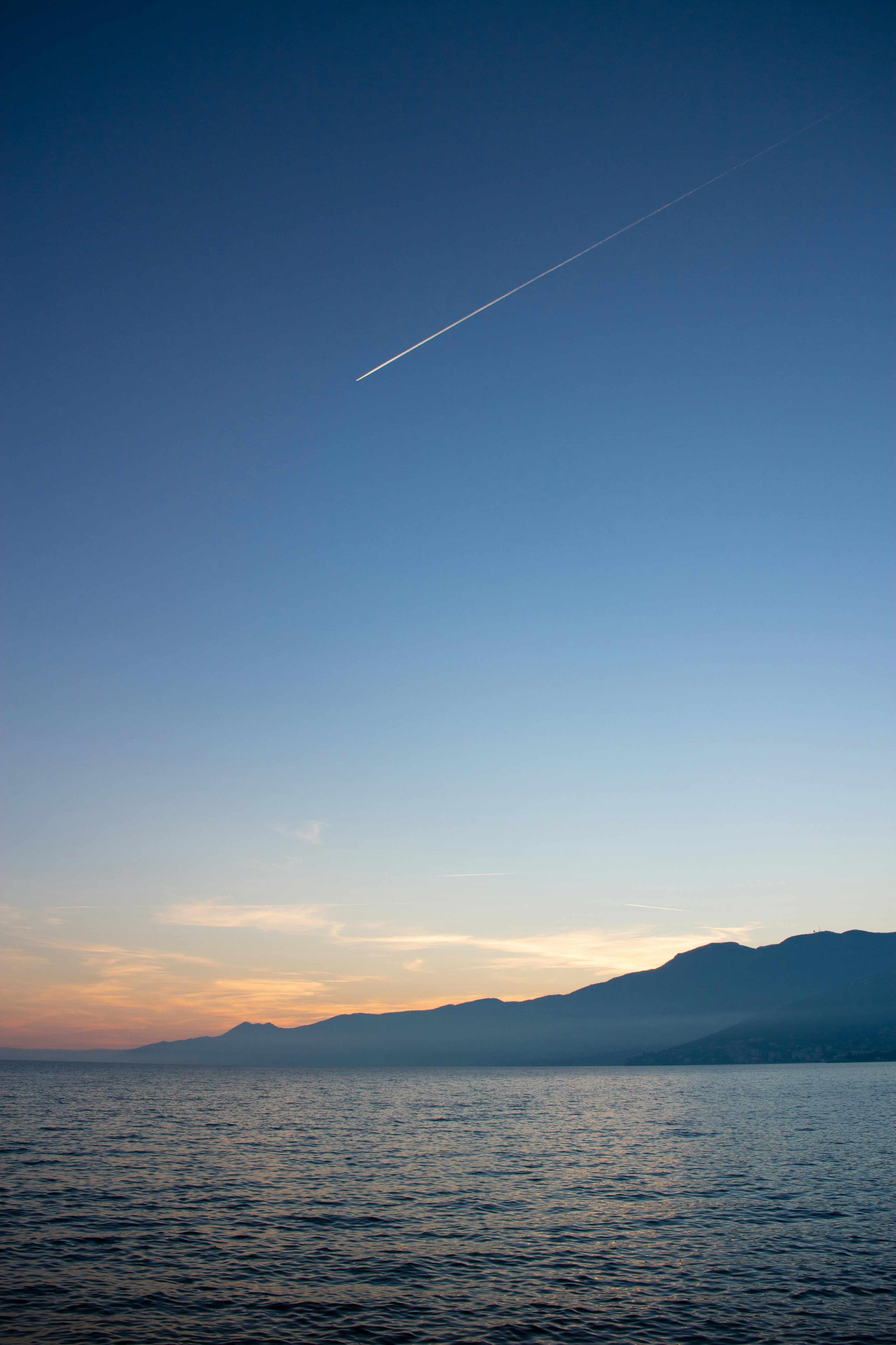 Blue Hour Jet Trail Over a Calm Sea and Distant Ridge