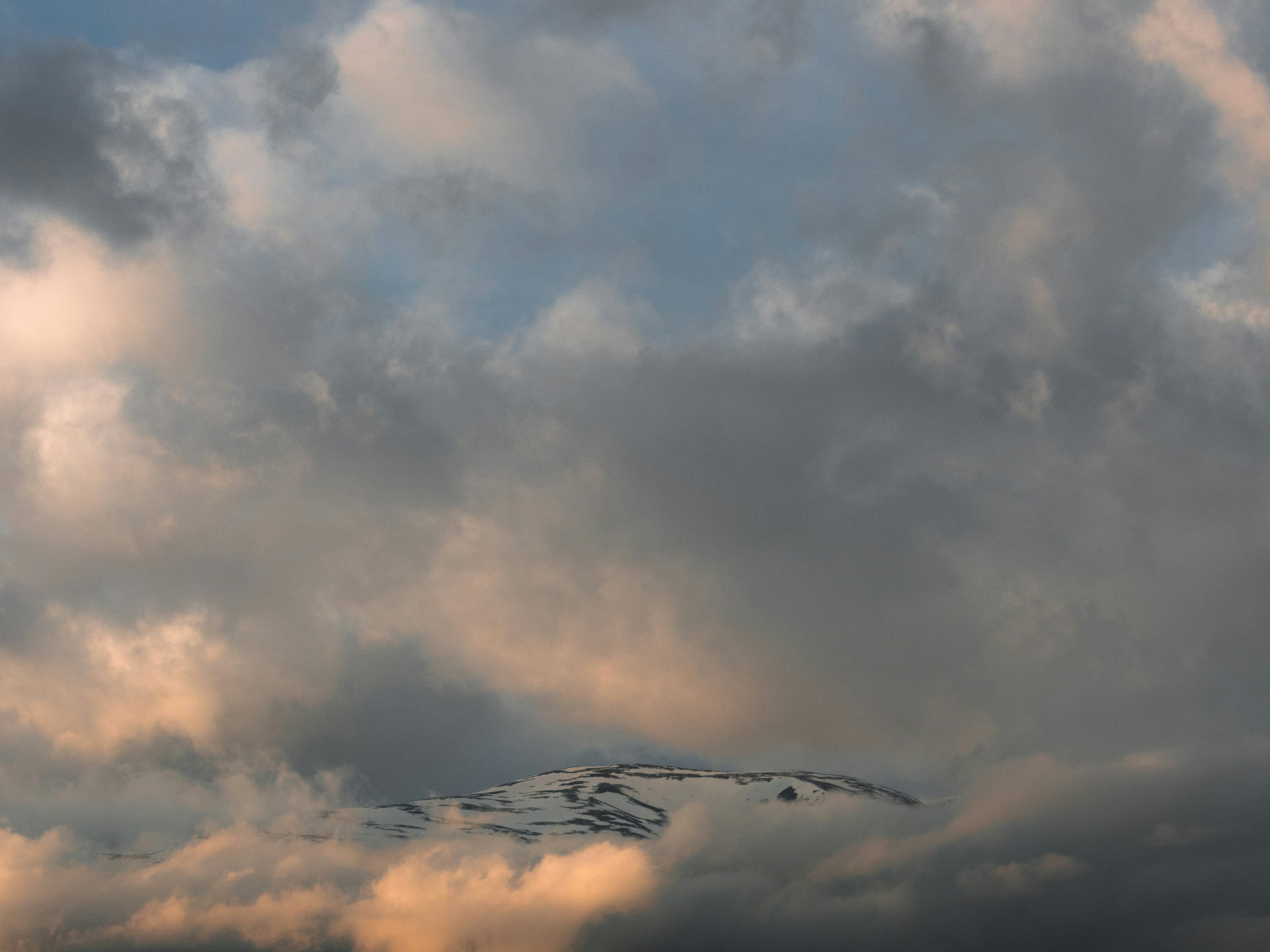 Snow-capped mountain partially obscured by dramatic clouds, with hints of soft light breaking through. 