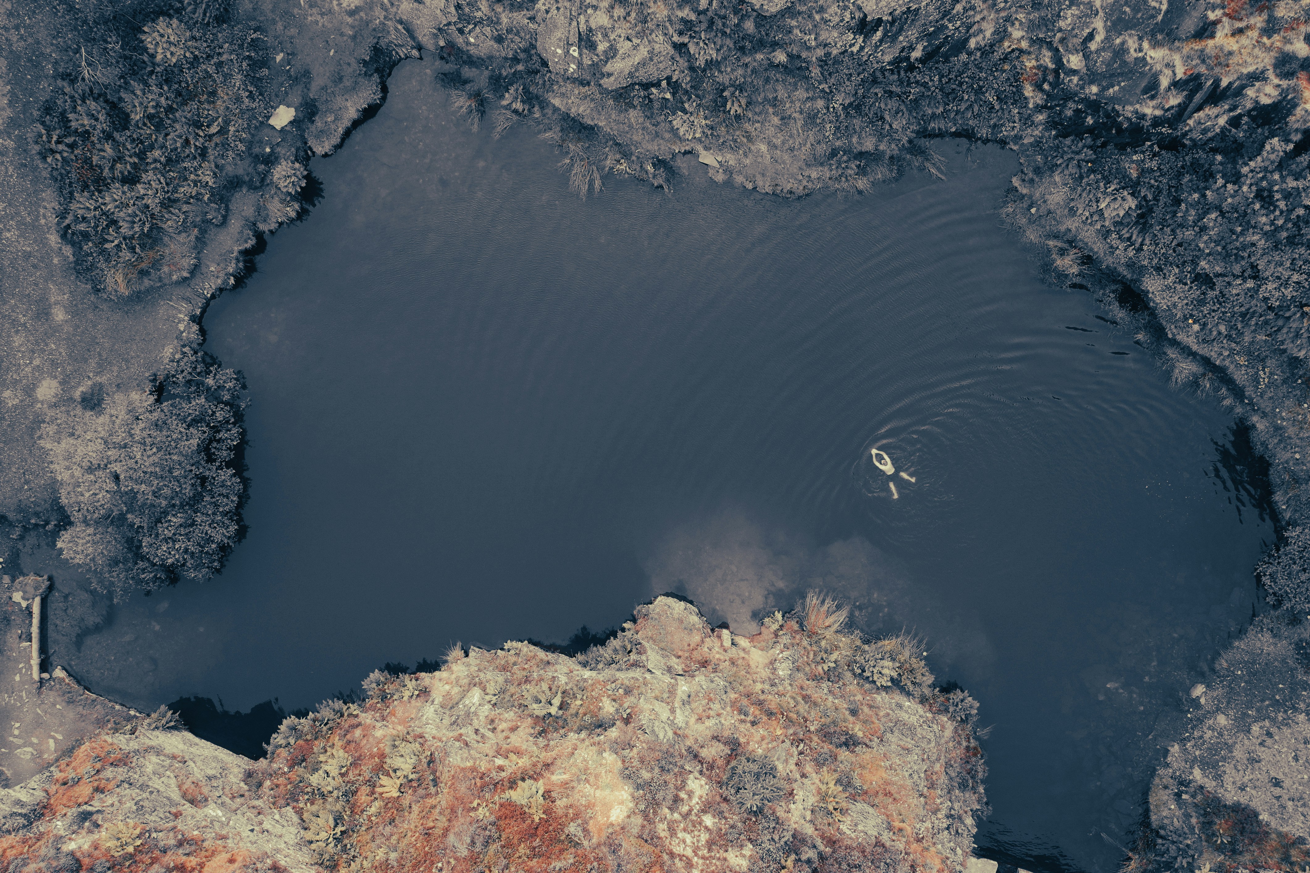 A lone kayak glides across a still, dark pond, surrounded by rocky terrain and sparse vegetation. The scene evokes a sense of tranquility.