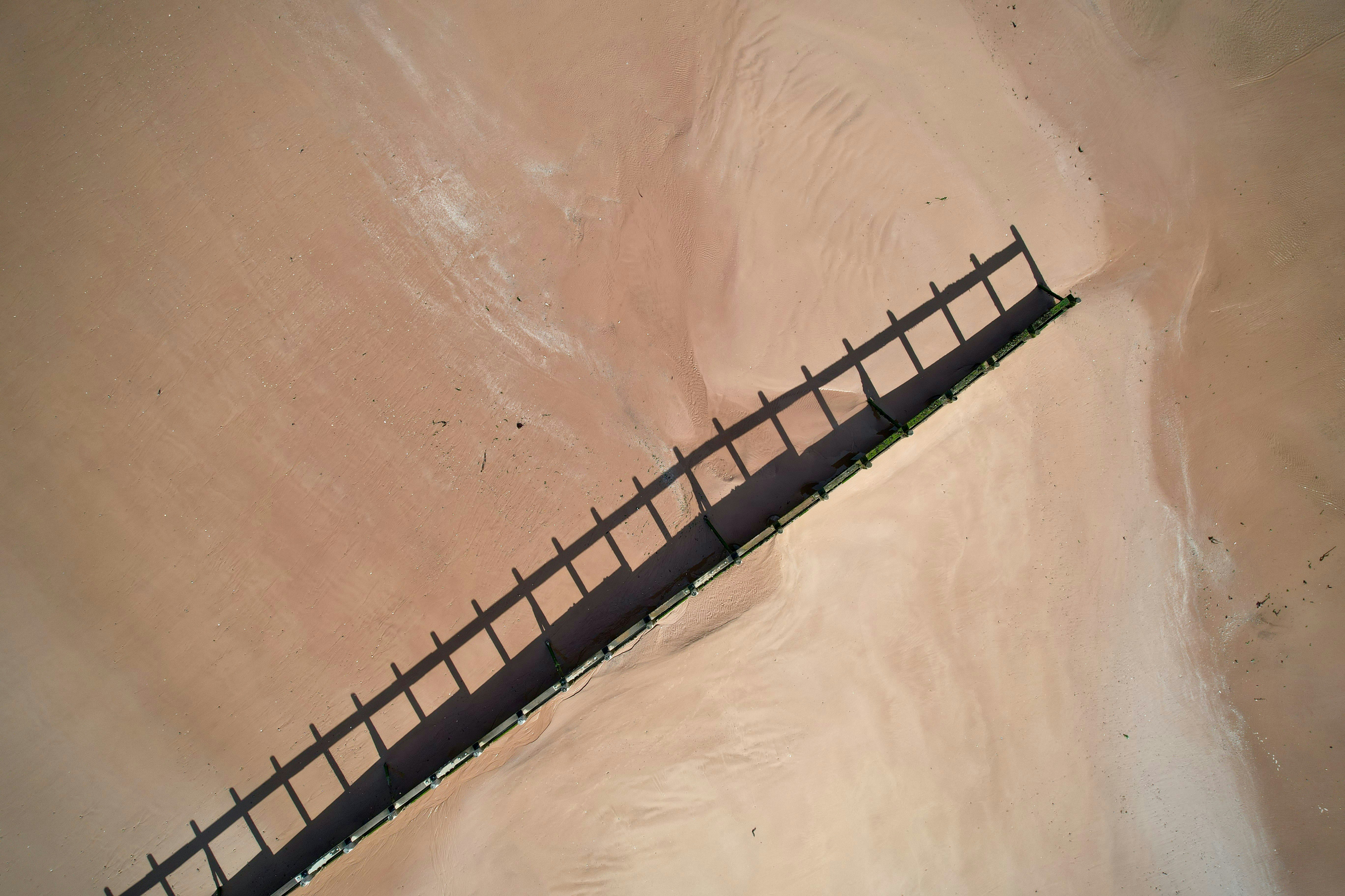 Aerial view of a beach with a winding fence casting a sharp shadow on the sand.
