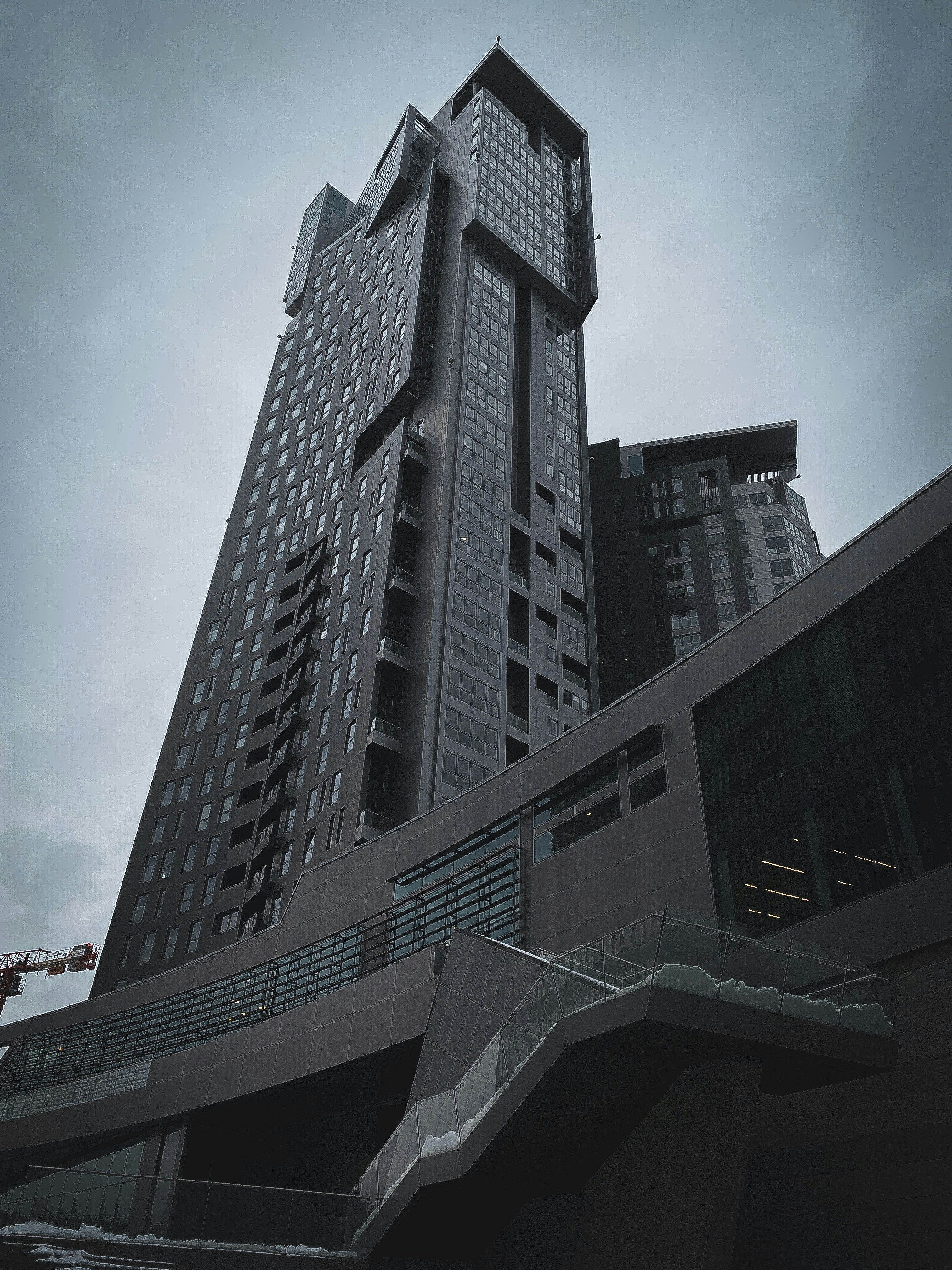 A towering skyscraper looms against a moody sky, showcasing sleek lines and contemporary design elements. The structure's angular features dominate the urban landscape.