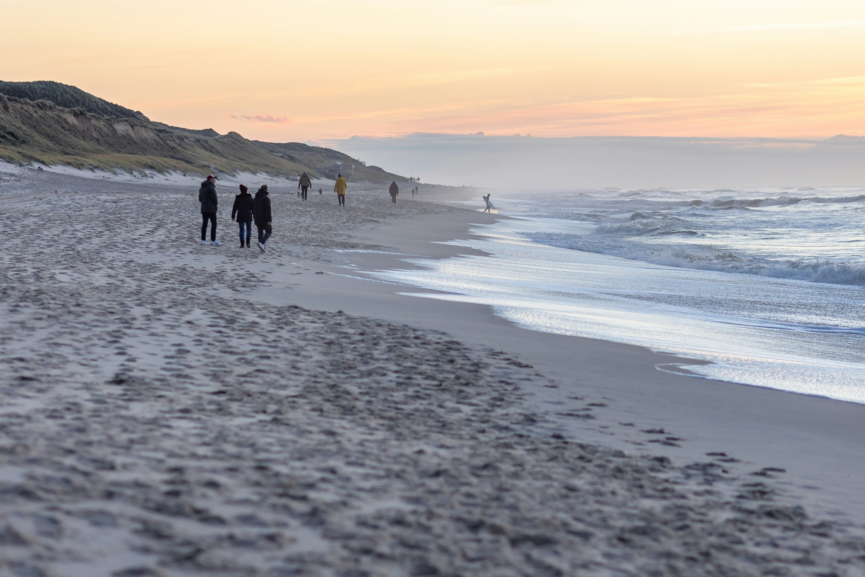 People walking on a serene beach at sunrise with gentle waves lapping the shoreline.