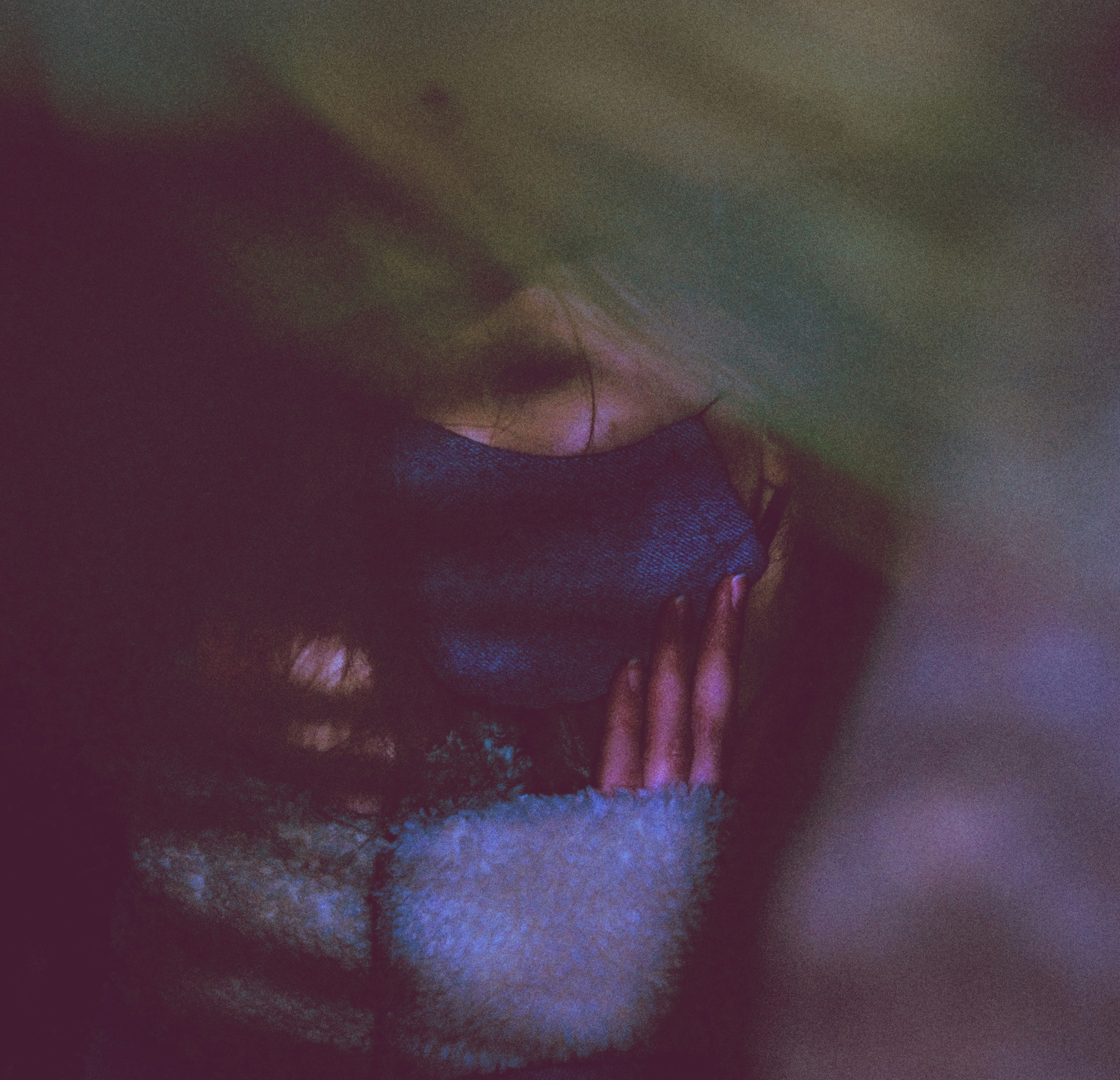 A person gently cradling a blue fabric, enveloped in soft shadows and muted colors, evoking a sense of introspection.