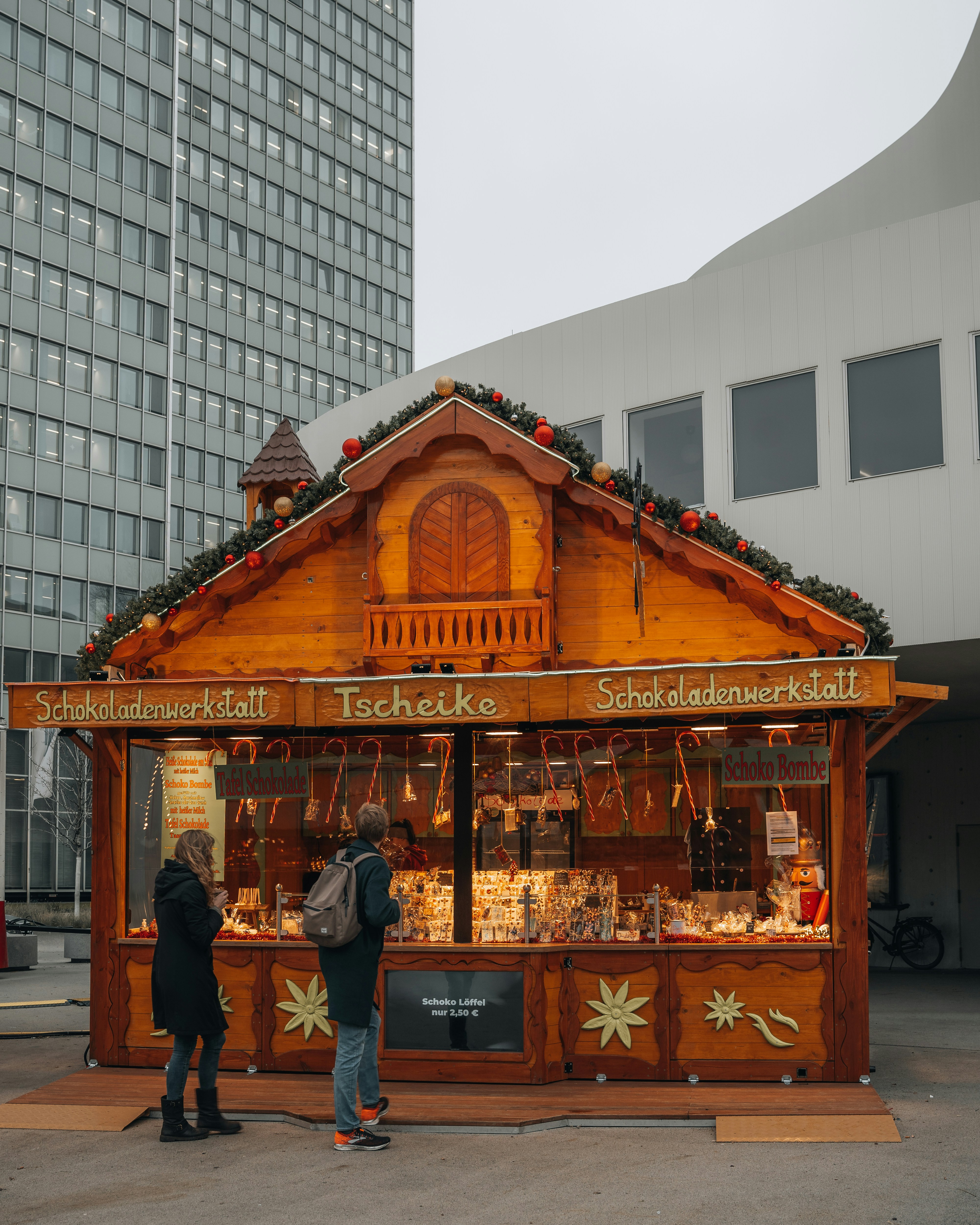 Charming wooden stall adorned with festive decorations, showcasing an array of chocolates and sweets. Visitors engage with the display, embodying a warm holiday spirit.