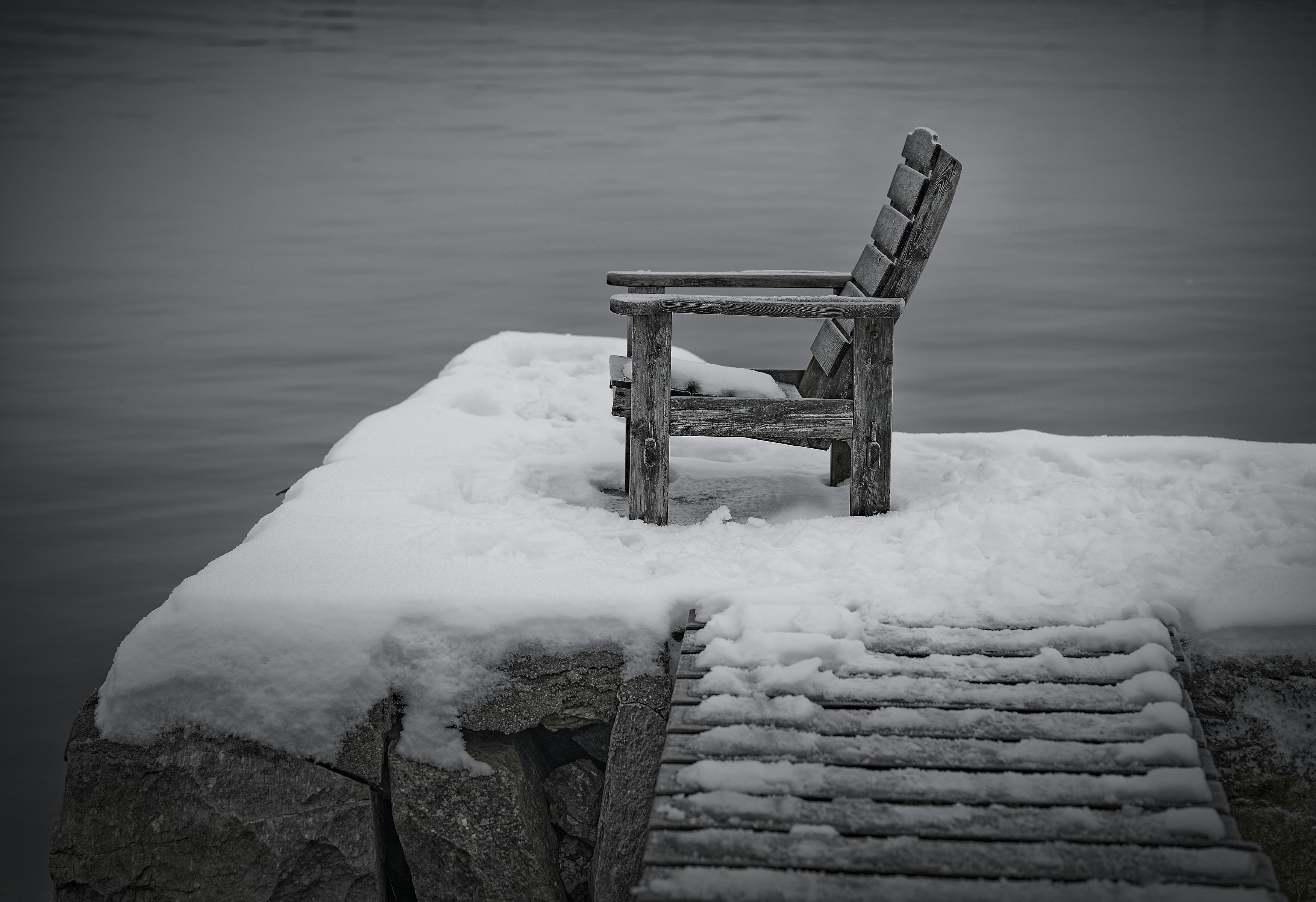 a wooden chair sitting on top of a snow covered pier