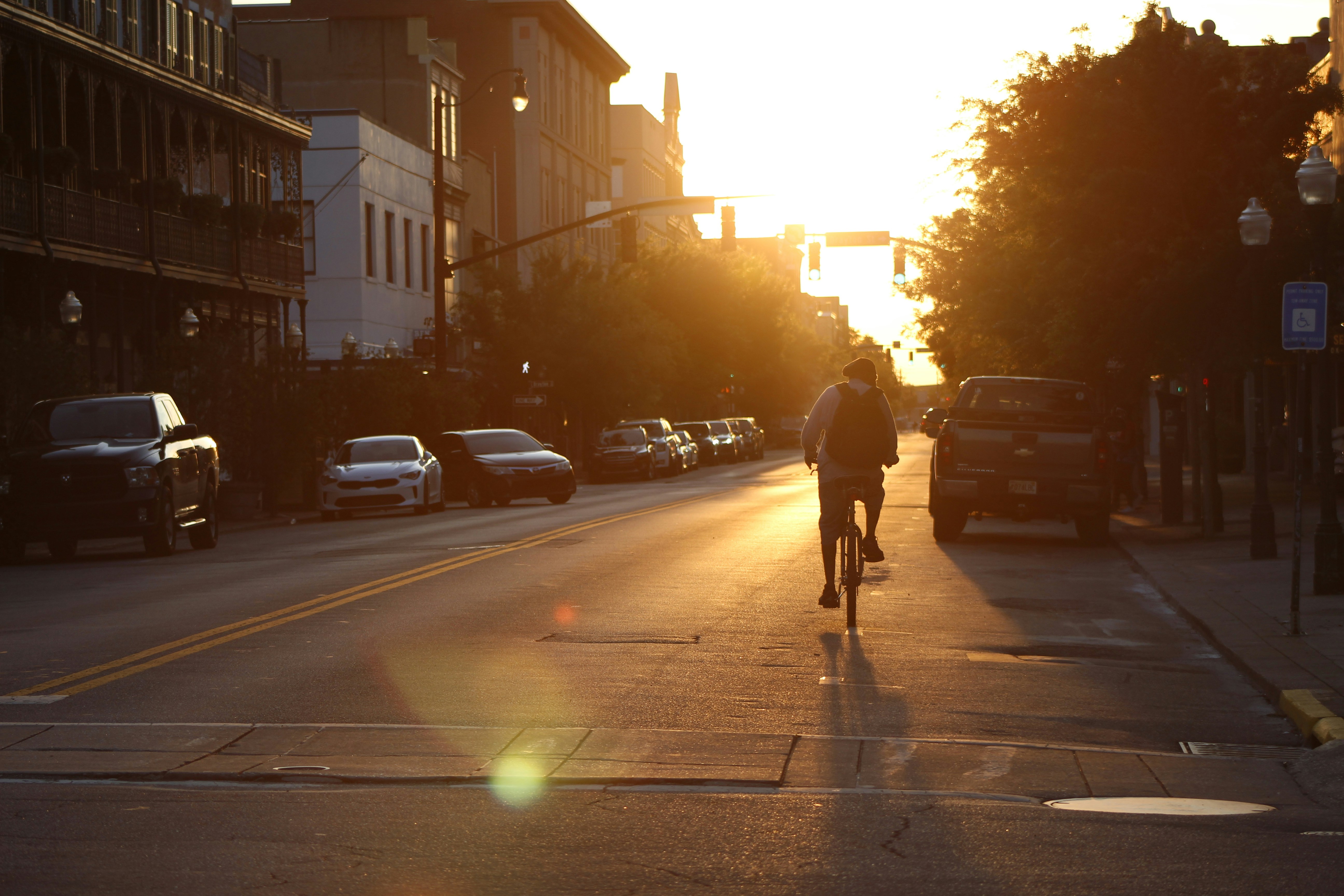 Cyclist rides down a sunlit urban street with a brilliant sunset in the background.
