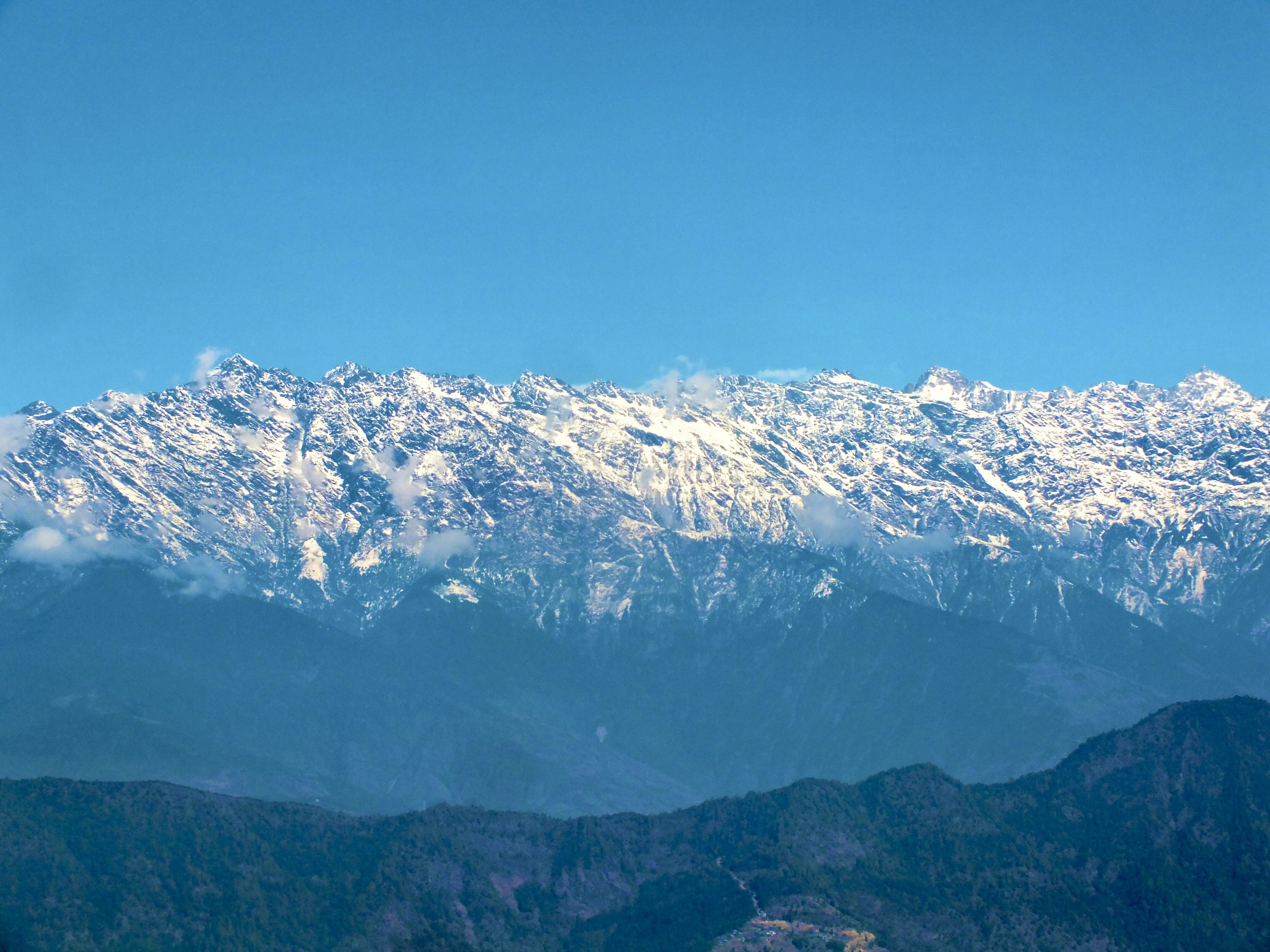 Snow-capped mountain range rising majestically against a clear blue sky, showcasing the grandeur of nature's beauty.