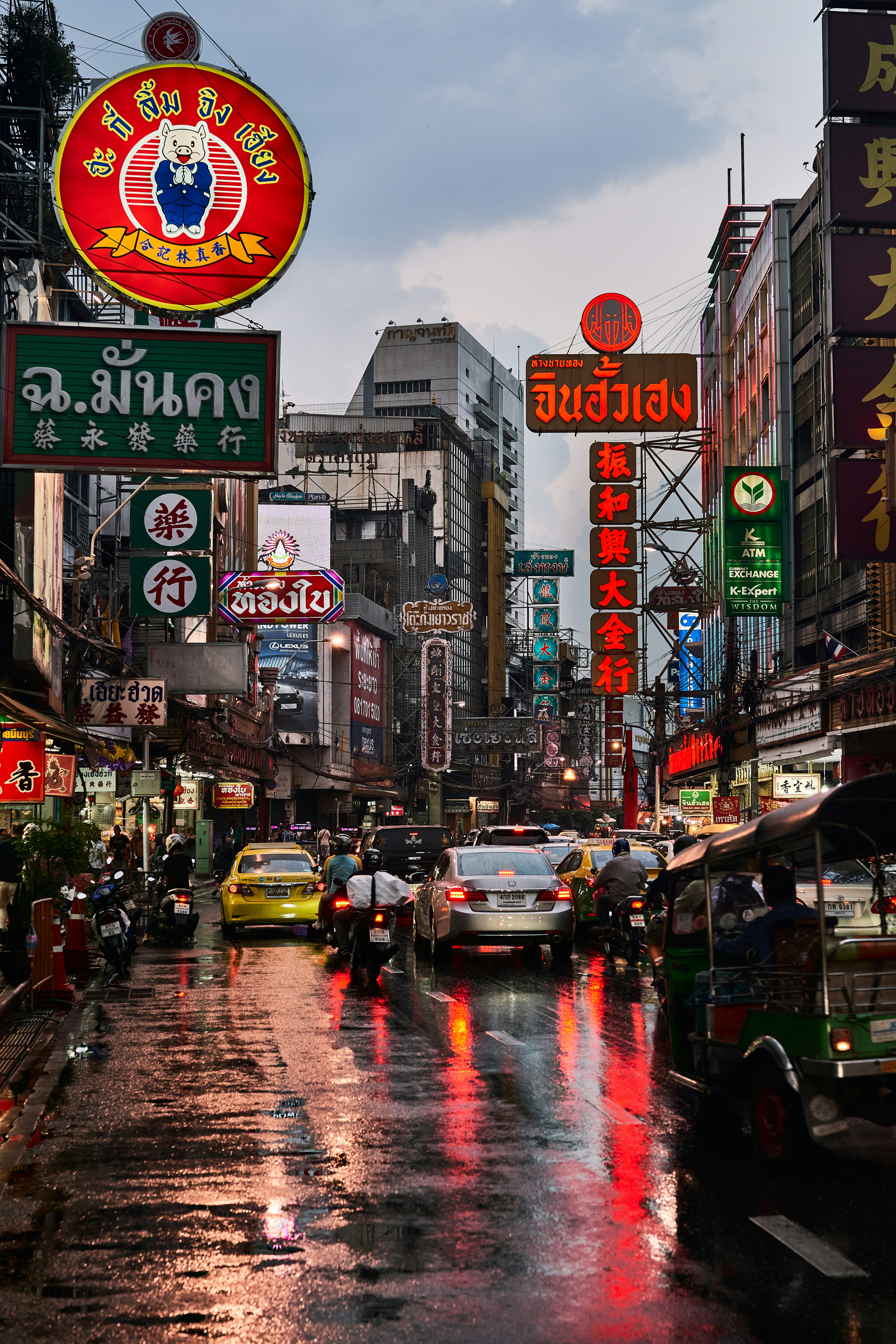 Vibrant street scene in a bustling city illuminated by neon signs, with wet pavement reflecting colorful lights during twilight.