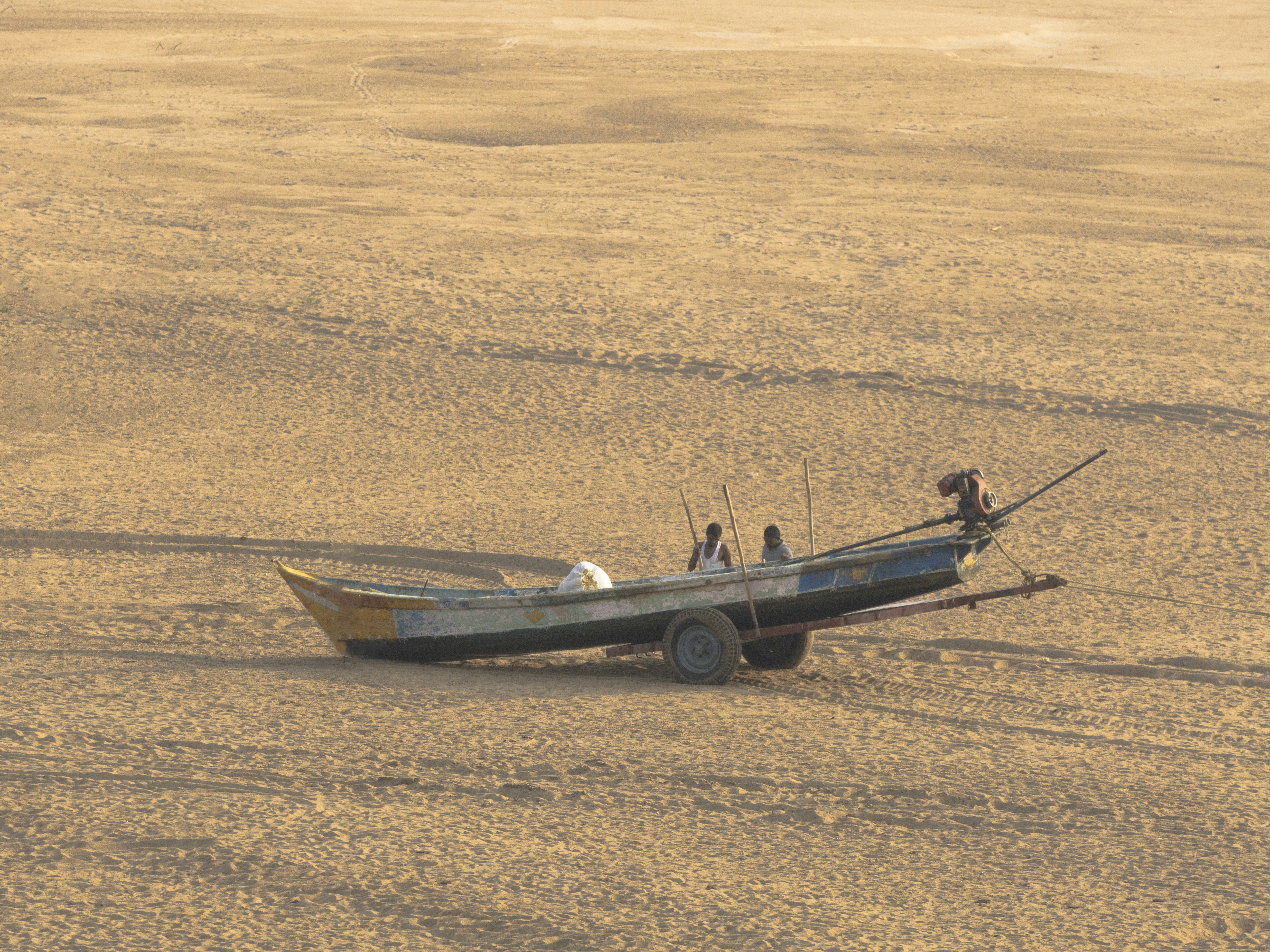 A weathered boat stranded on a vast expanse of golden sand, with two figures preparing to navigate the arid landscape.