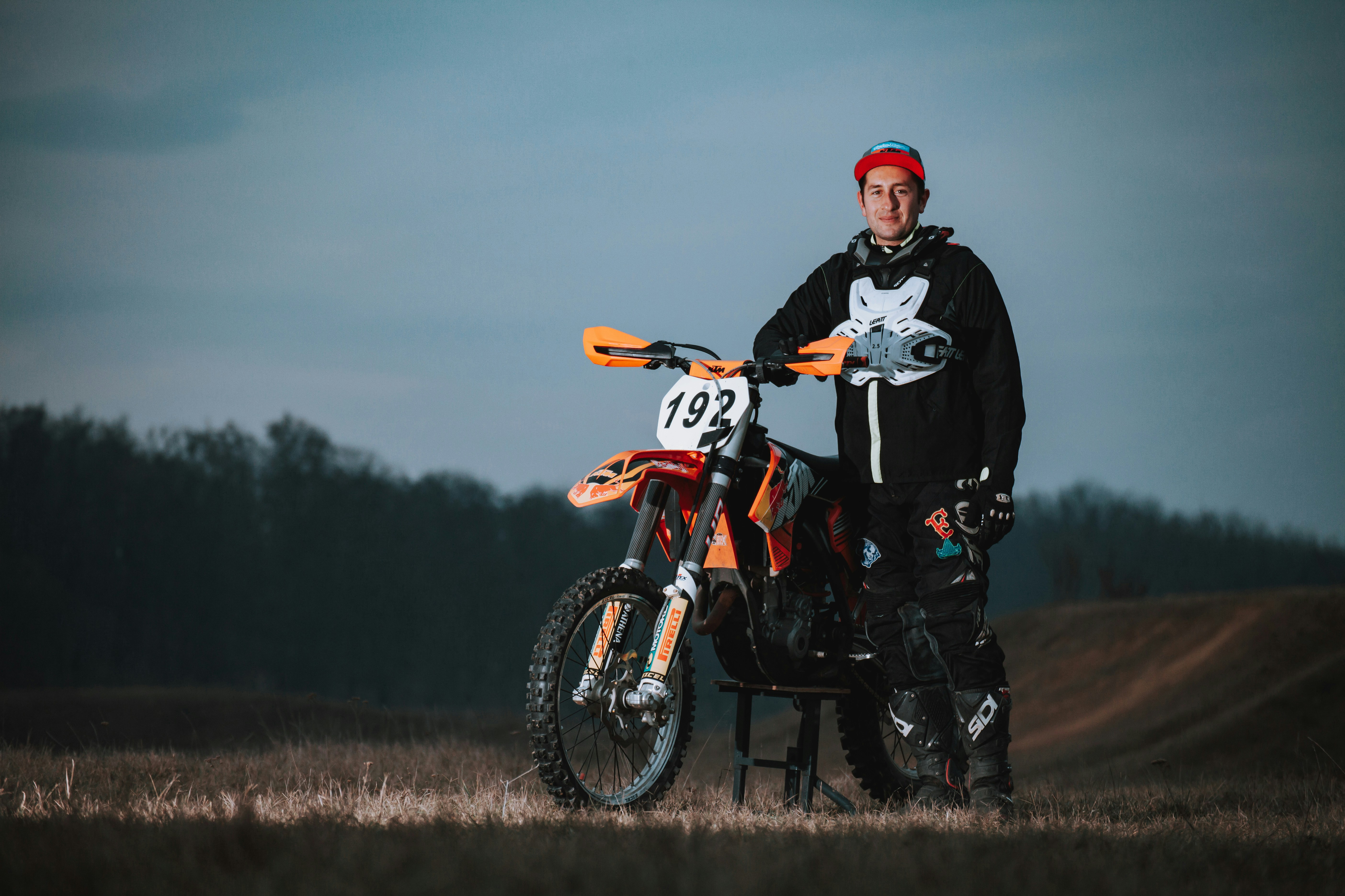 Quiet Readiness: Motocross Rider Pauses with Orange Dirt Bike at Dusk