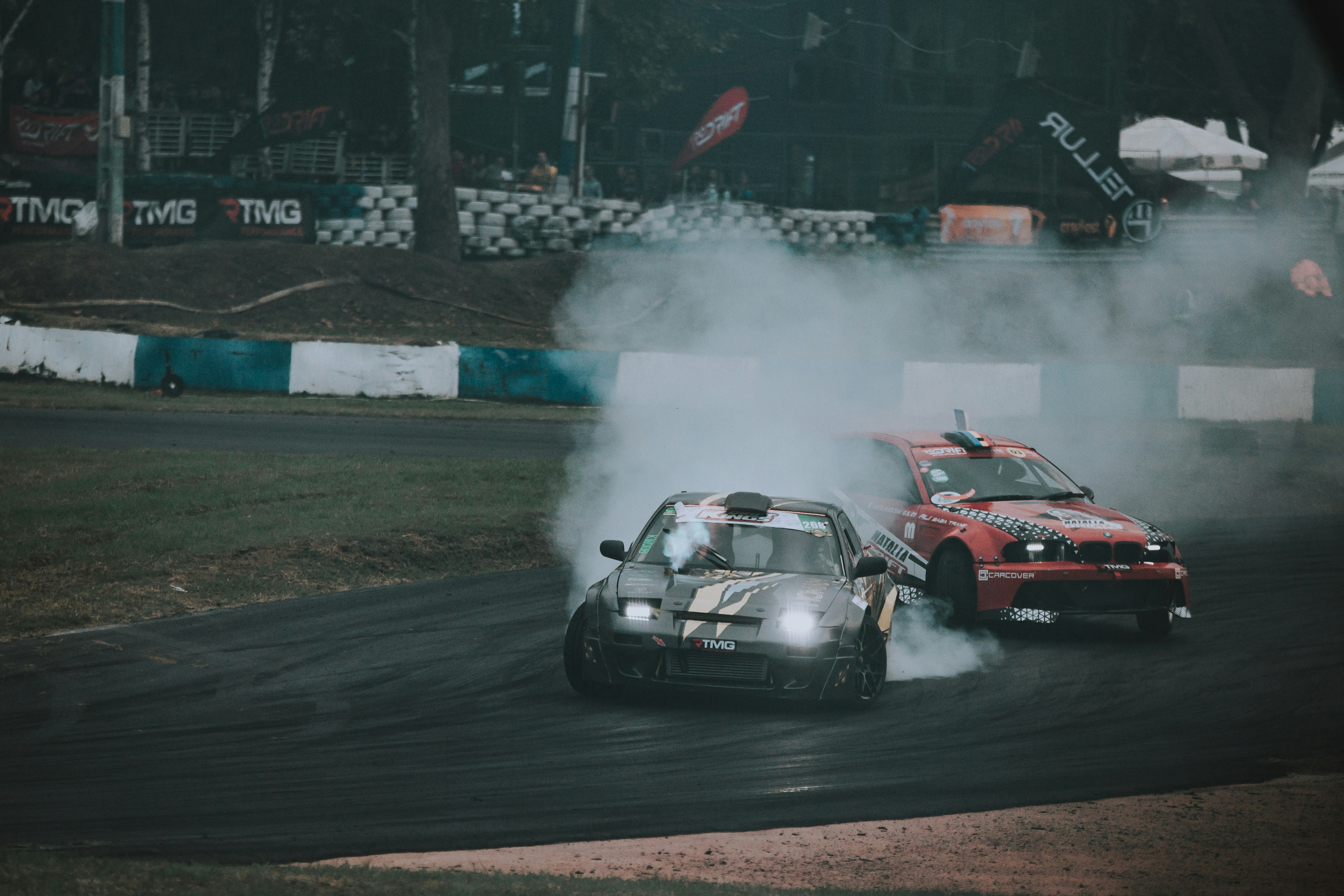 Two race cars drift around a corner, enveloped in a cloud of tire smoke during a competitive event.