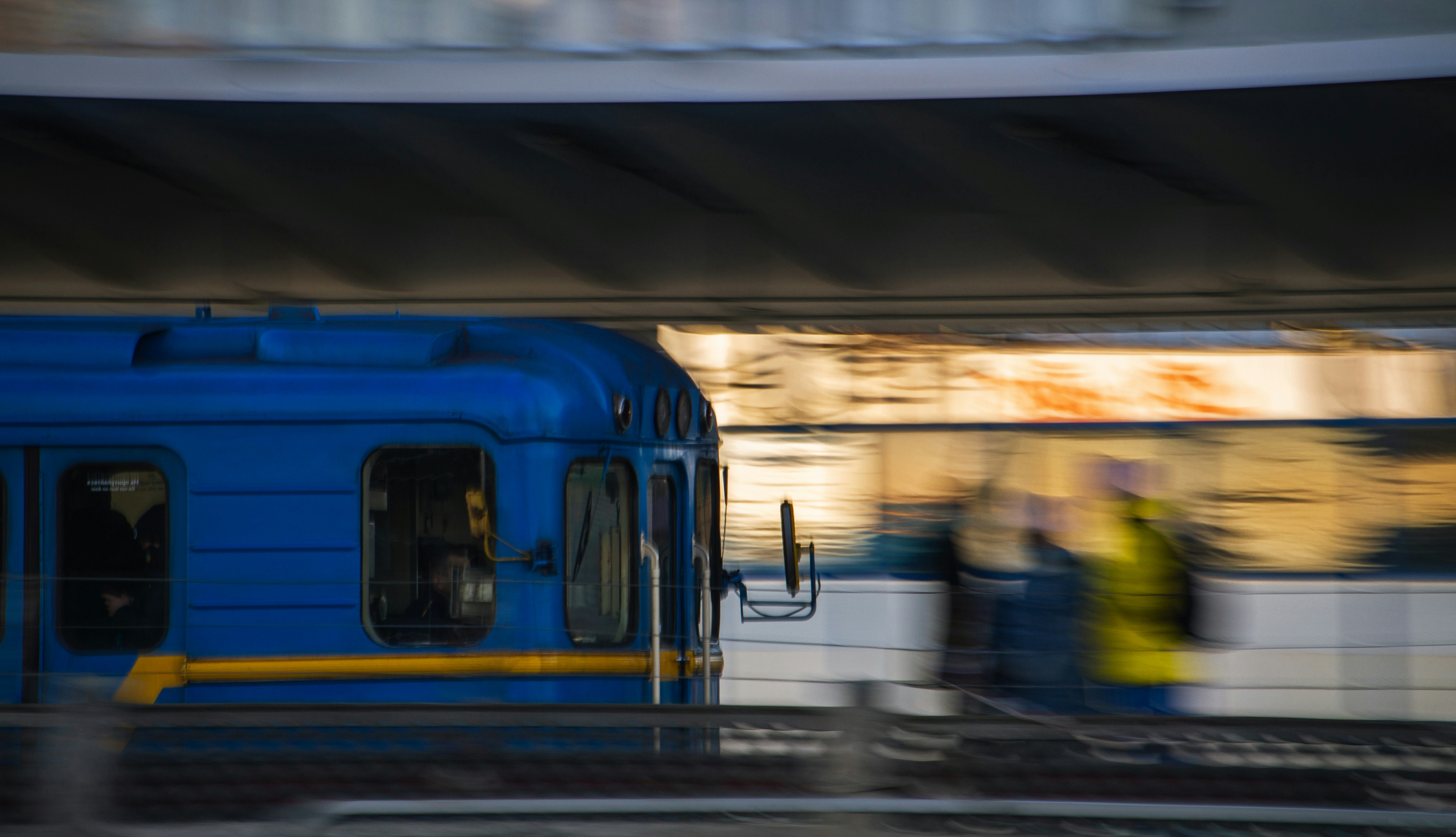 A blue train traveling down train tracks next to a loading platform ...