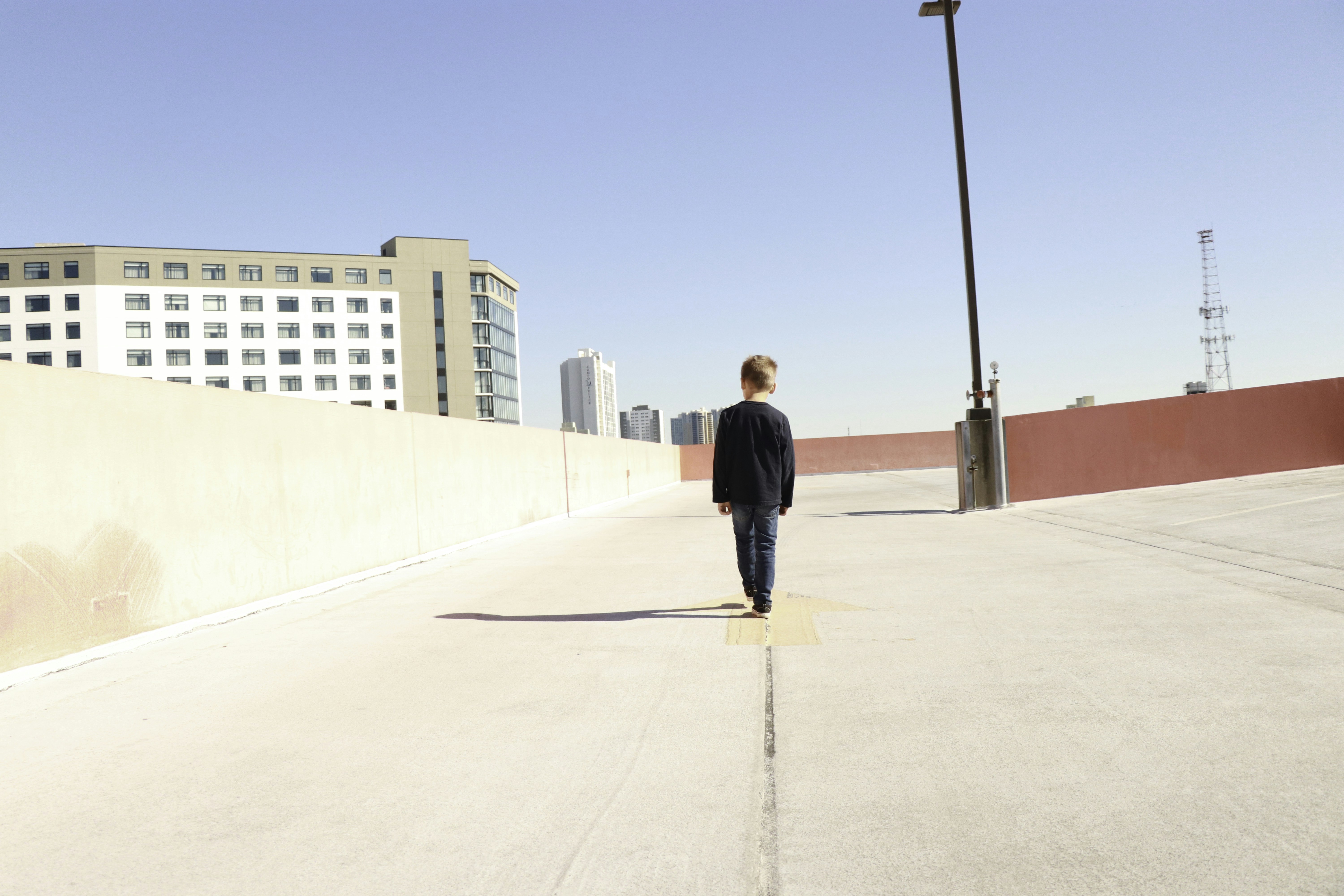 A child walks alone on a rooftop, surrounded by a stark urban landscape. The clear blue sky contrasts with the concrete structures.