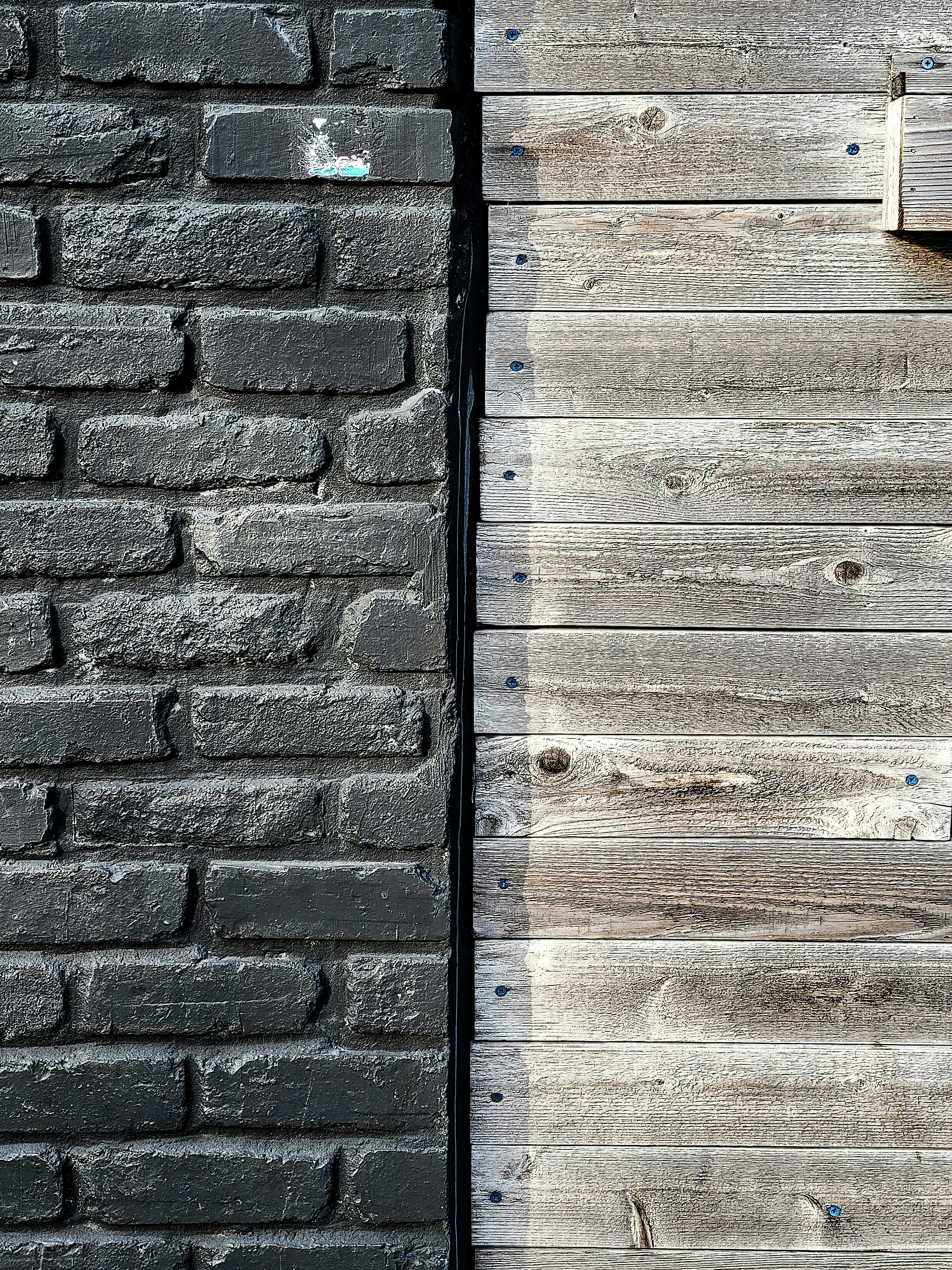 Rough black brick wall juxtaposed with smooth wooden planks, showcasing the beauty of contrasting materials and textures.