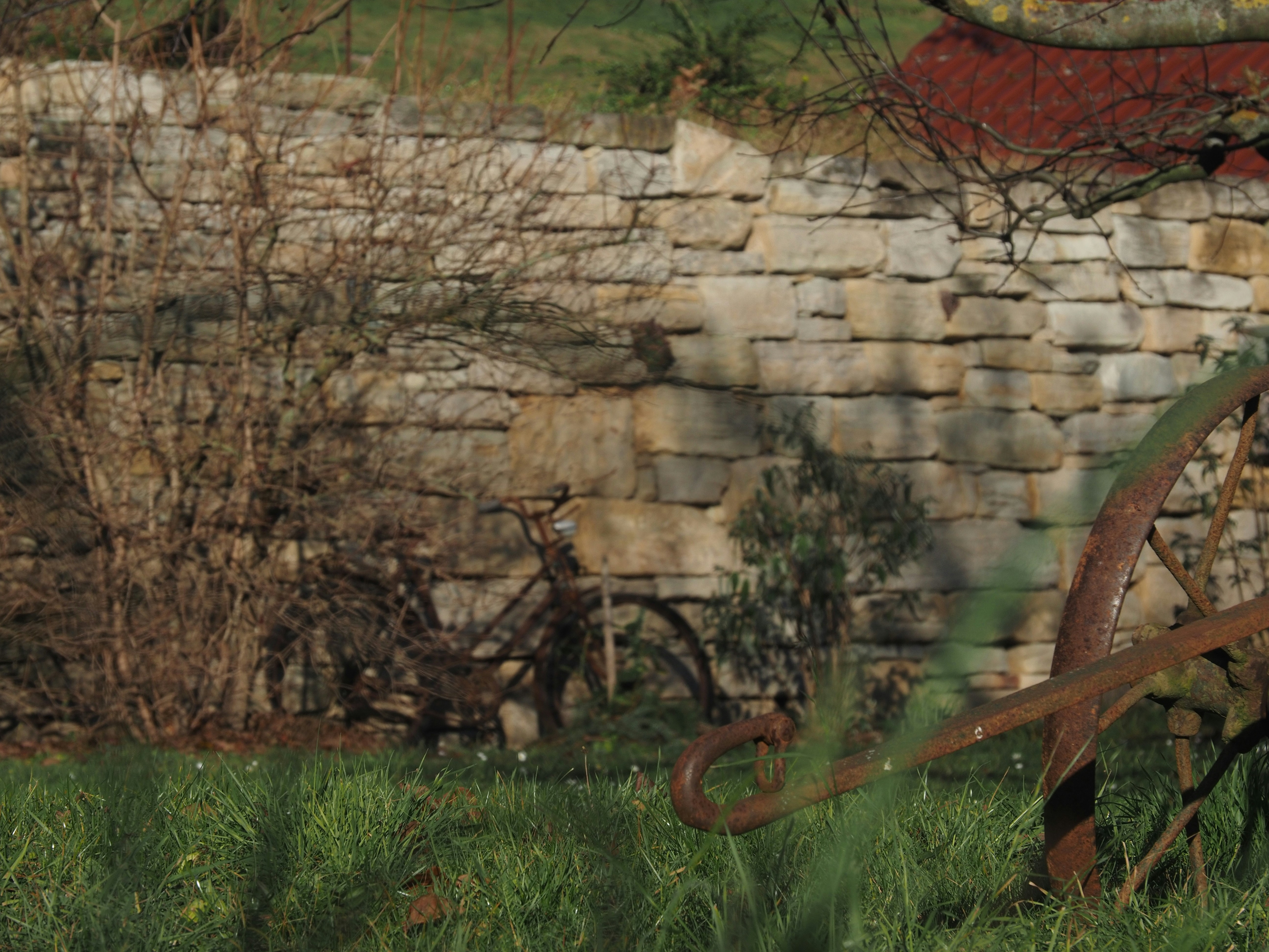 an old rusted wagon sitting in the grass next to a stone wall