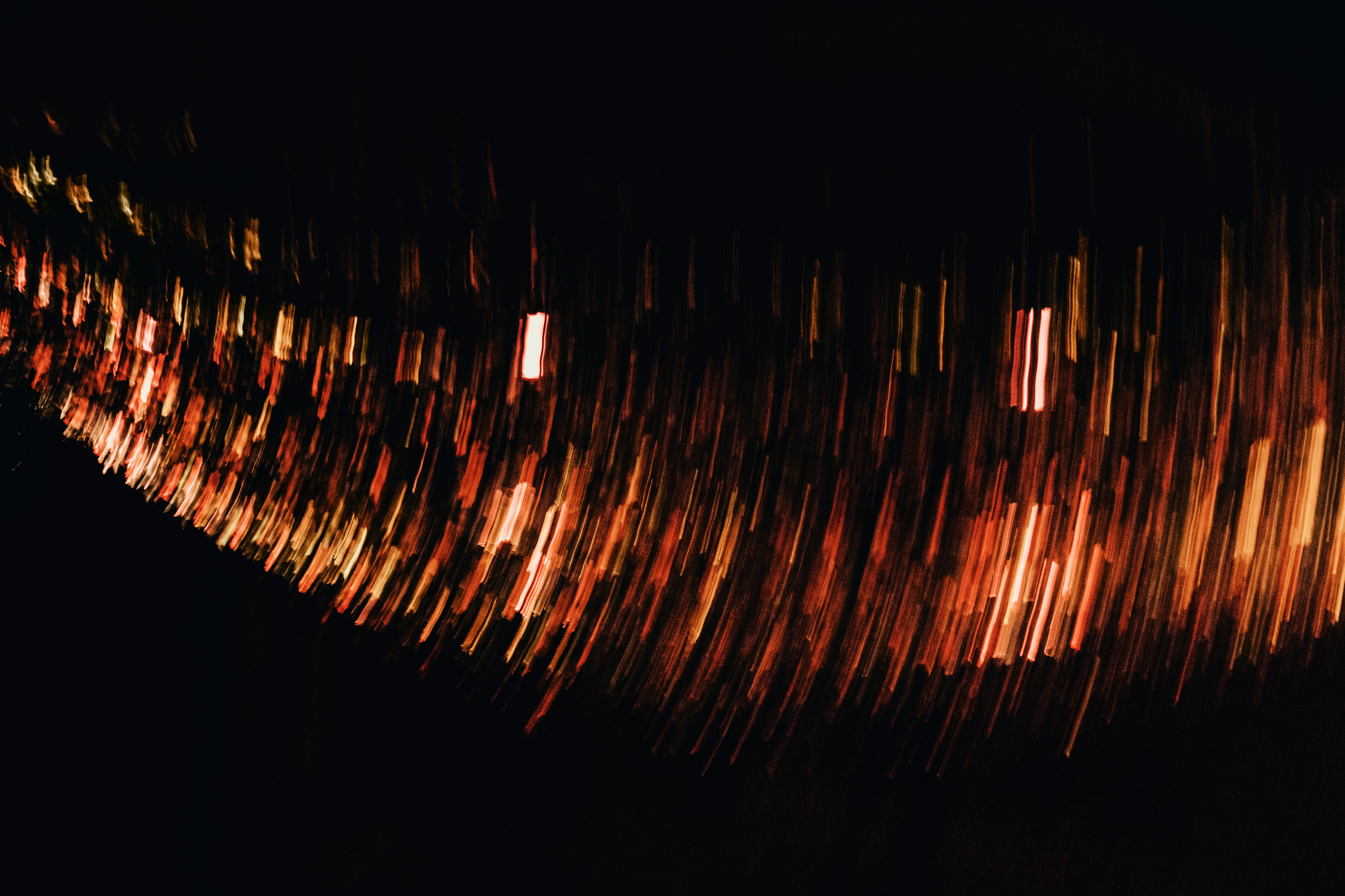 Long-exposure photograph of copper-orange light trails curving across a dark background. Abstract motion study emphasizes velocity and glow.