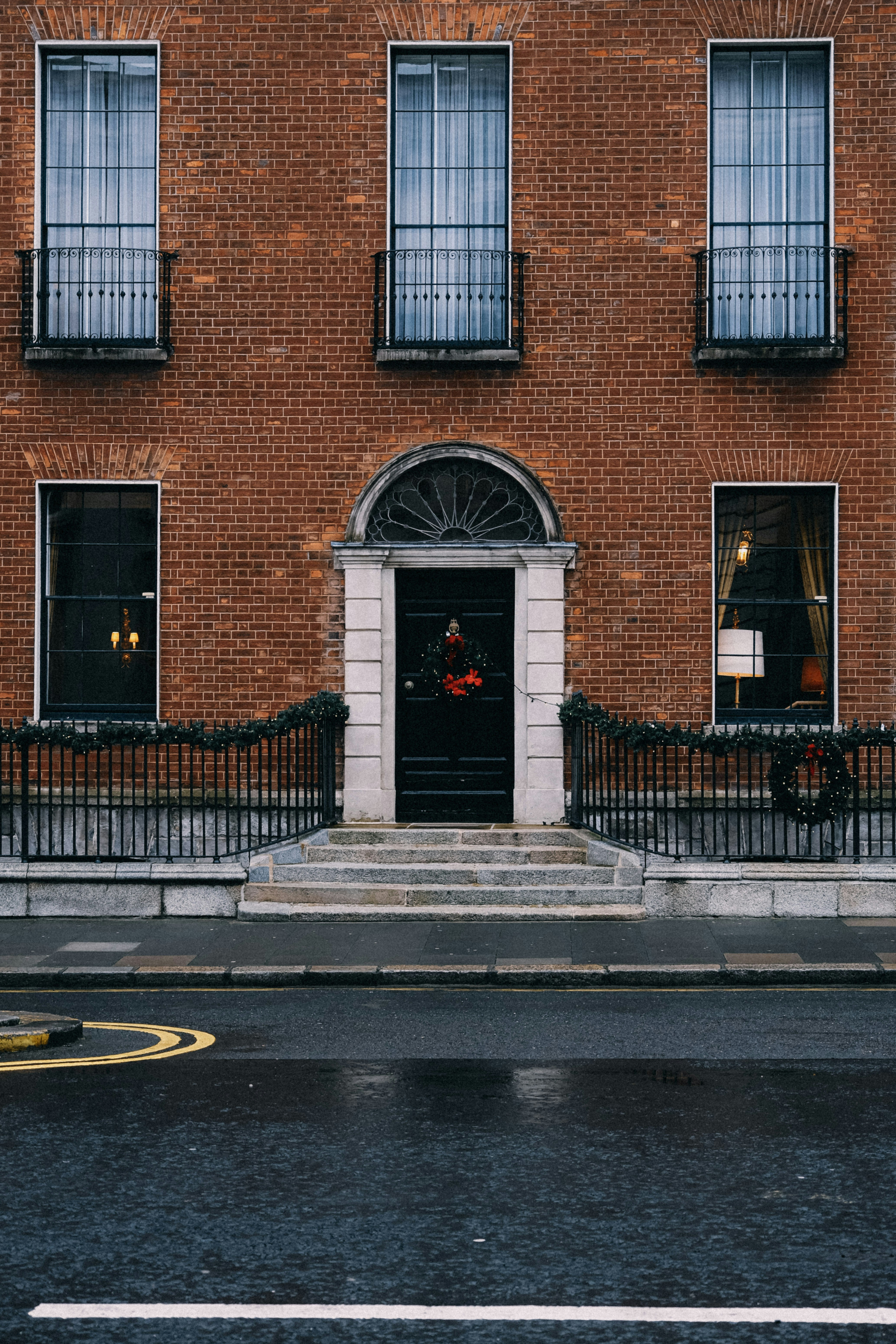 Charming brick facade adorned with festive greenery and a wreath, featuring elegant windows and a classic entrance. The scene captures a cozy atmosphere during the winter season.