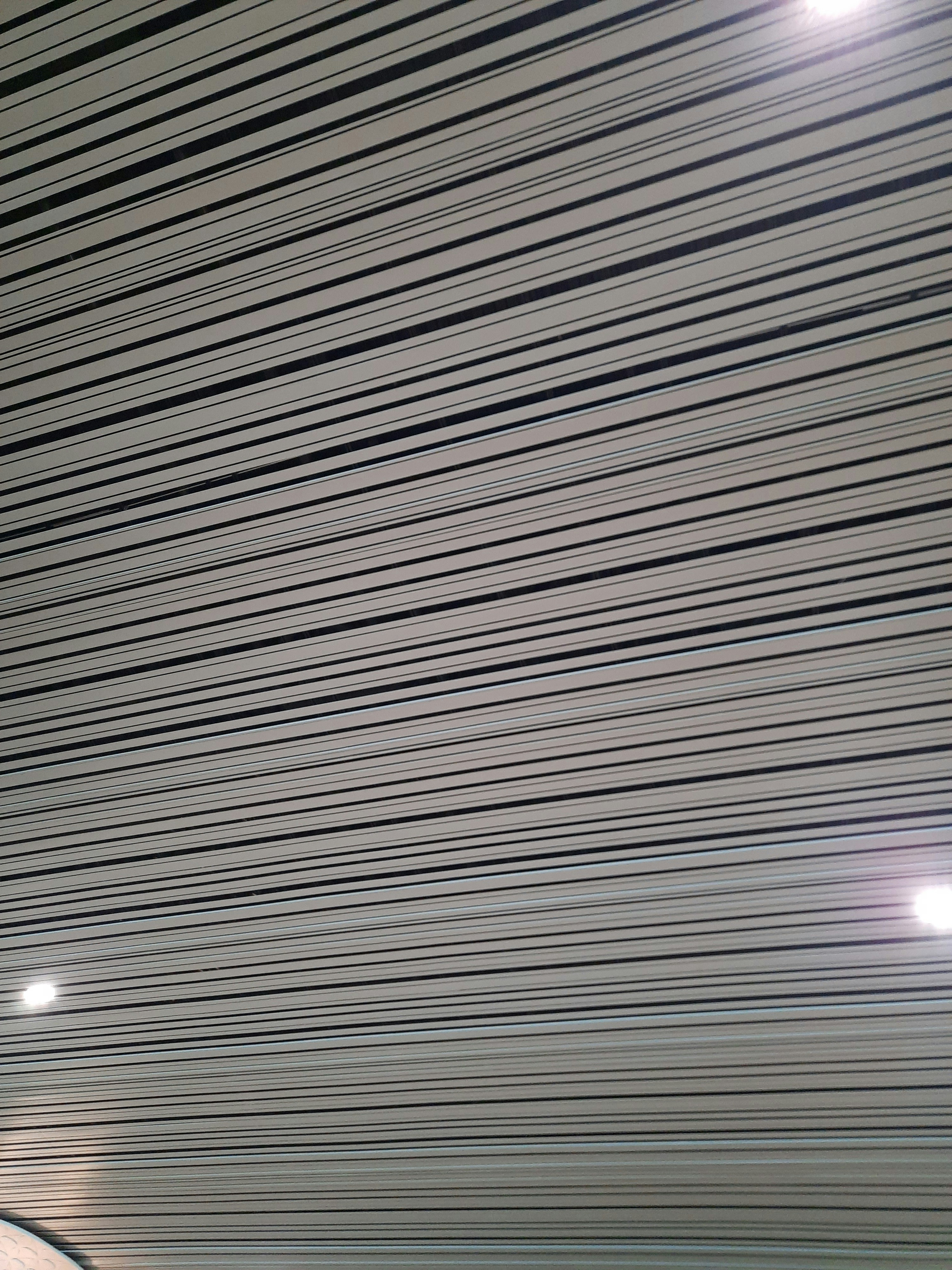 Diagonal stripes sweep across a dimly lit ceiling, forming a strong geometric rhythm. Subtle light sources at the edges add gentle highlights and depth.