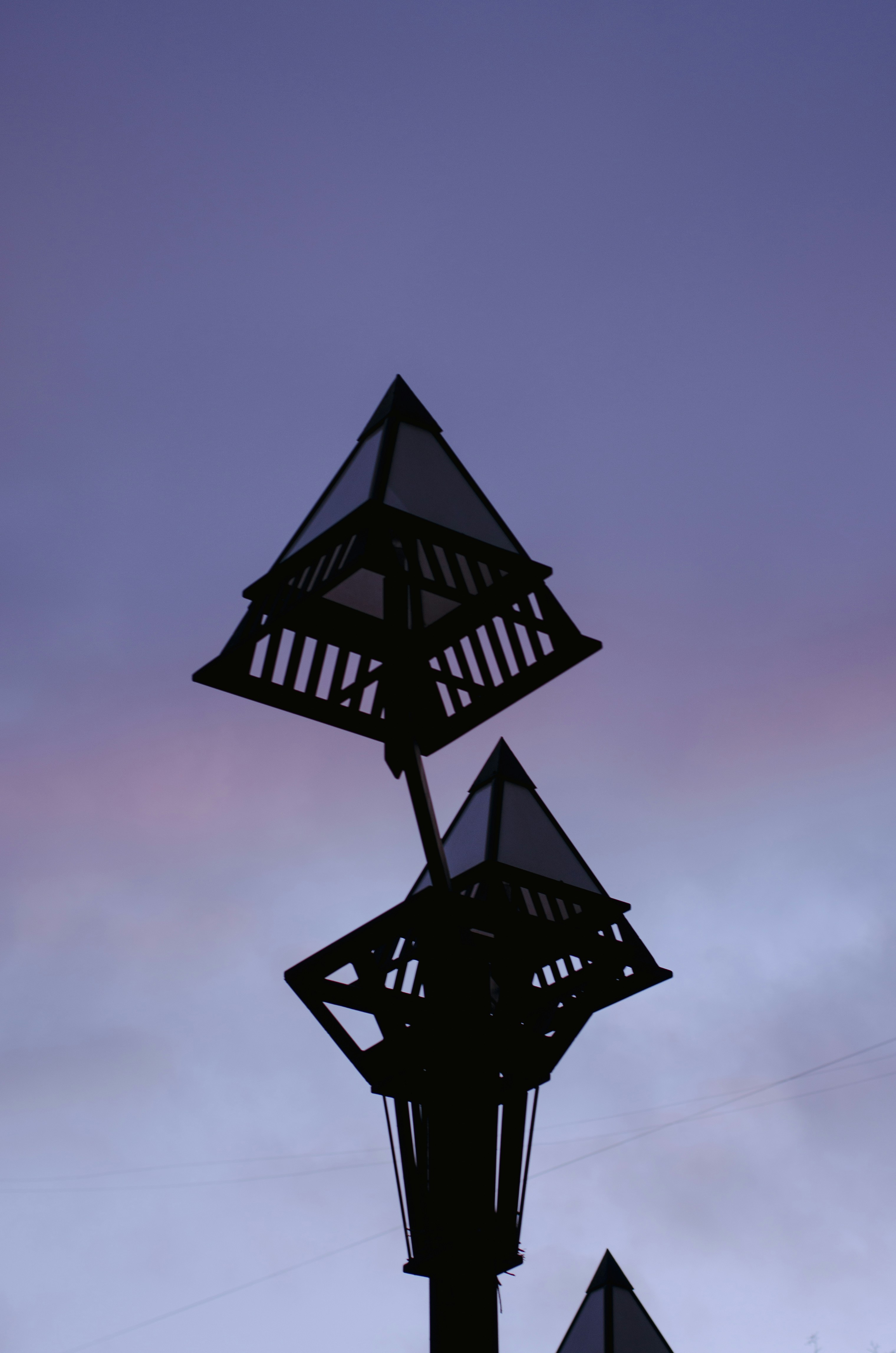 Three intricately designed lamp posts silhouetted against a gradient twilight sky, showcasing architectural elegance.