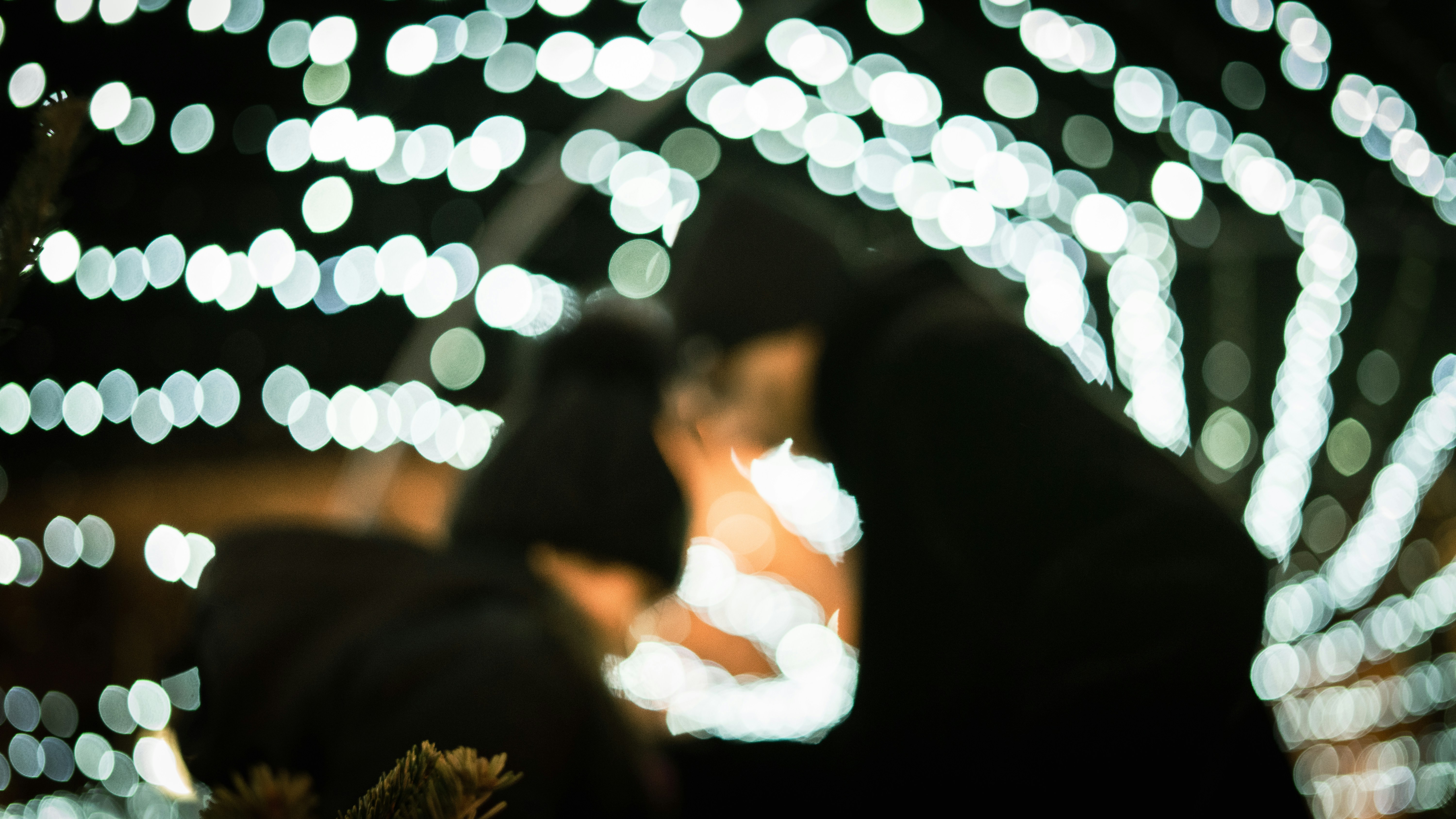 A blurry photo of a couple kissing in front of christmas lights photo ...
