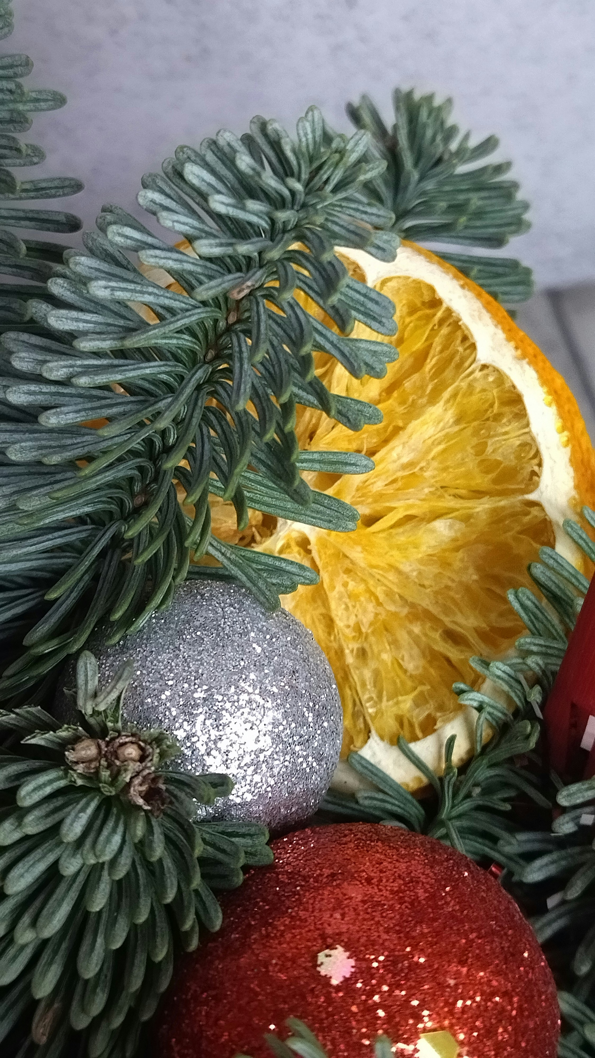 Glitter, Pine, and Citrus: A Festive Close-Up of Ornaments among Evergreen Sprigs