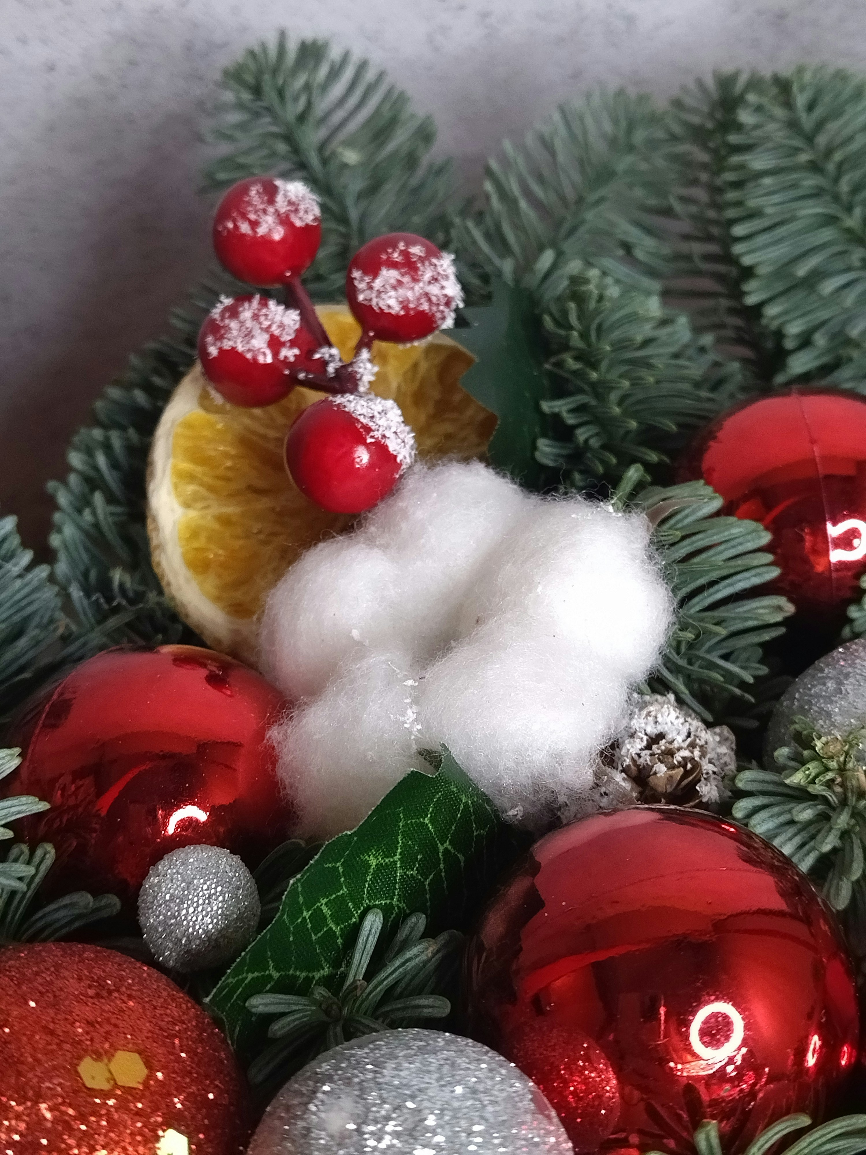 Christmas centerpiece with glossy red ornaments, cotton puff, pine needles, and a dried orange slice.