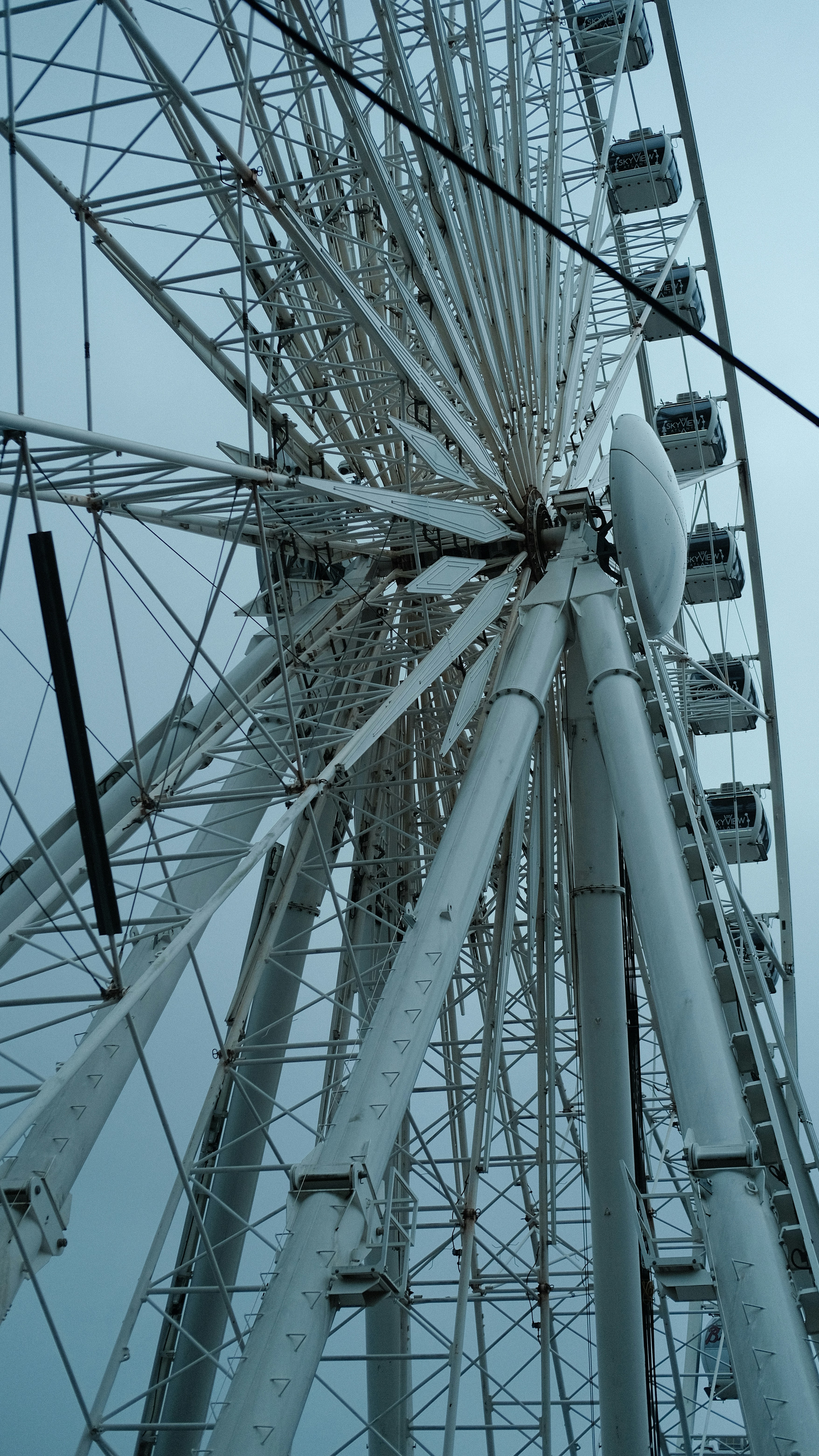 A towering ferris wheel viewed from below, showcasing its intricate framework against a moody sky.