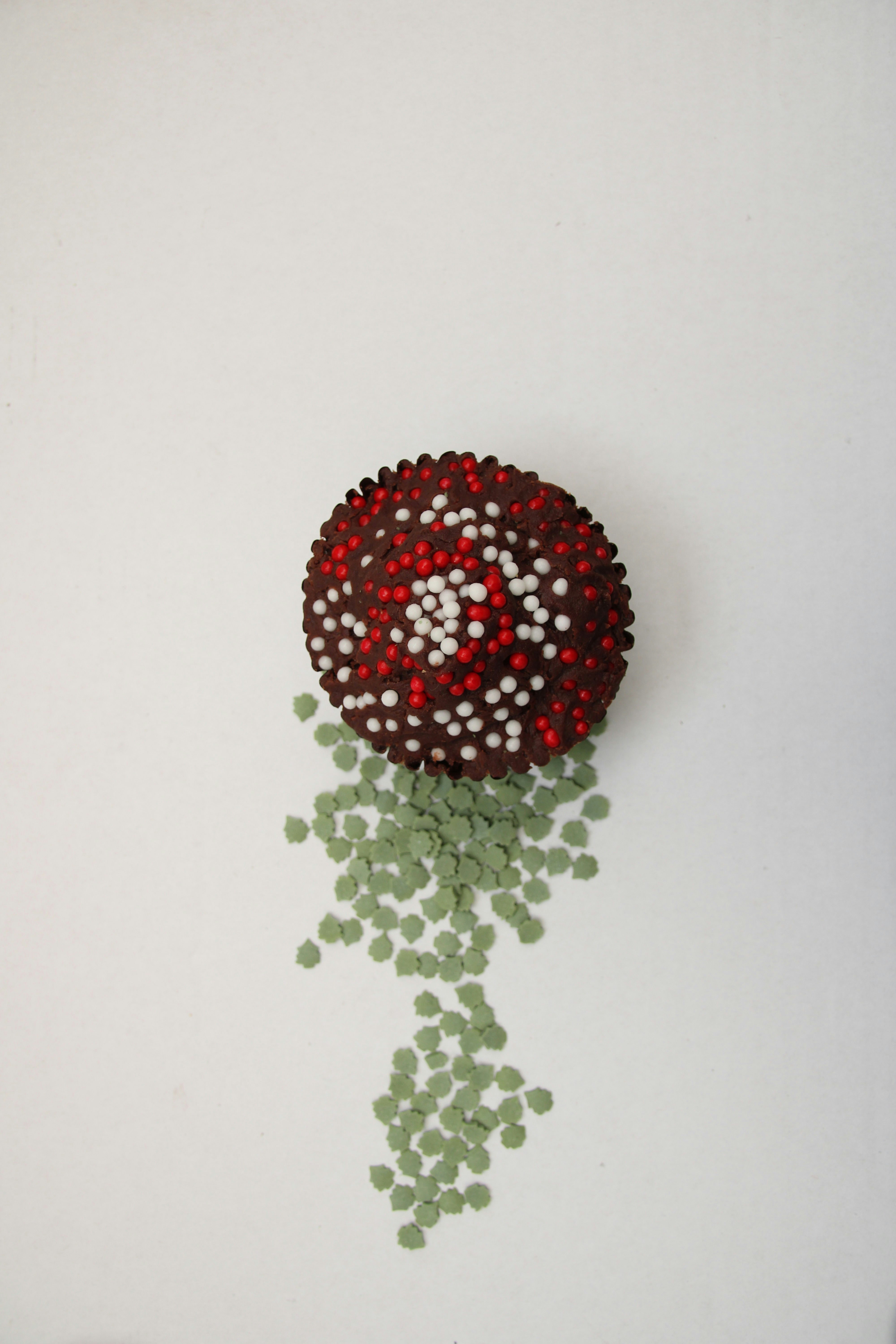 Chocolate cupcake adorned with red and white sprinkles, surrounded by green edible confetti.
