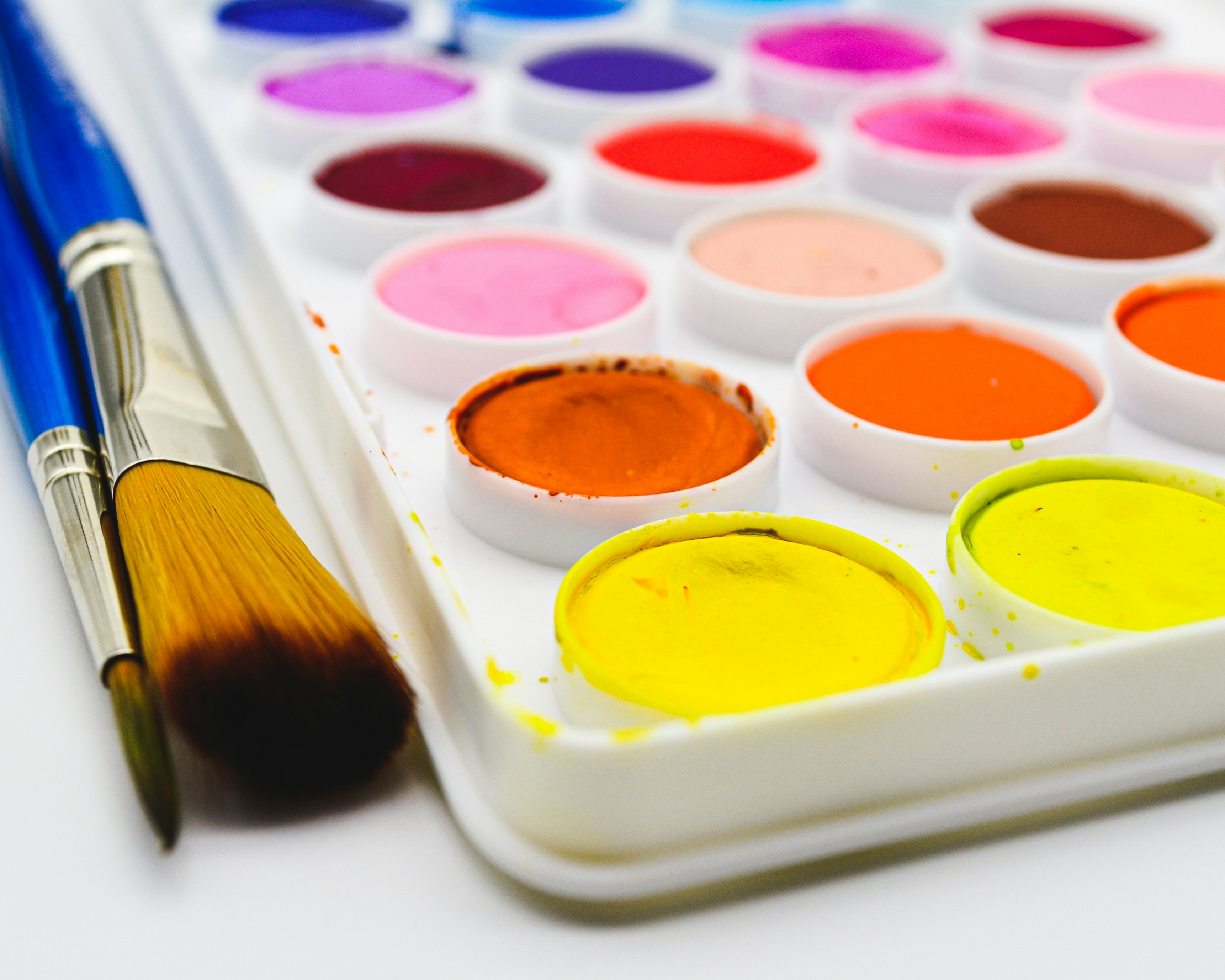 Vibrant watercolor paints arranged in a palette alongside two brushes, showcasing an artist's tools for creativity.