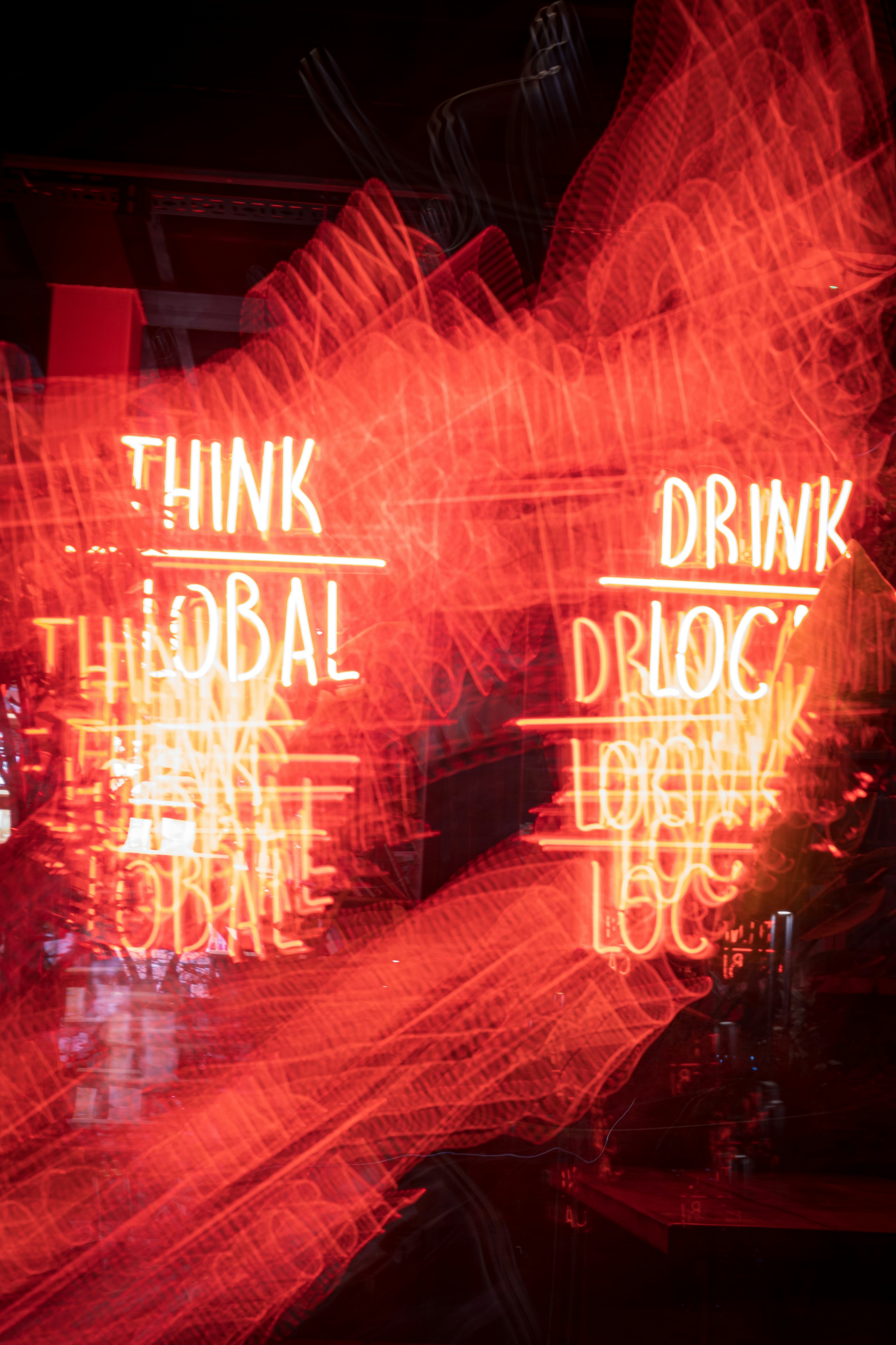 Dynamic neon text blurs between 'Think Global' and 'Drink Local,' creating a vibrant display that captures the energy of urban nightlife.
