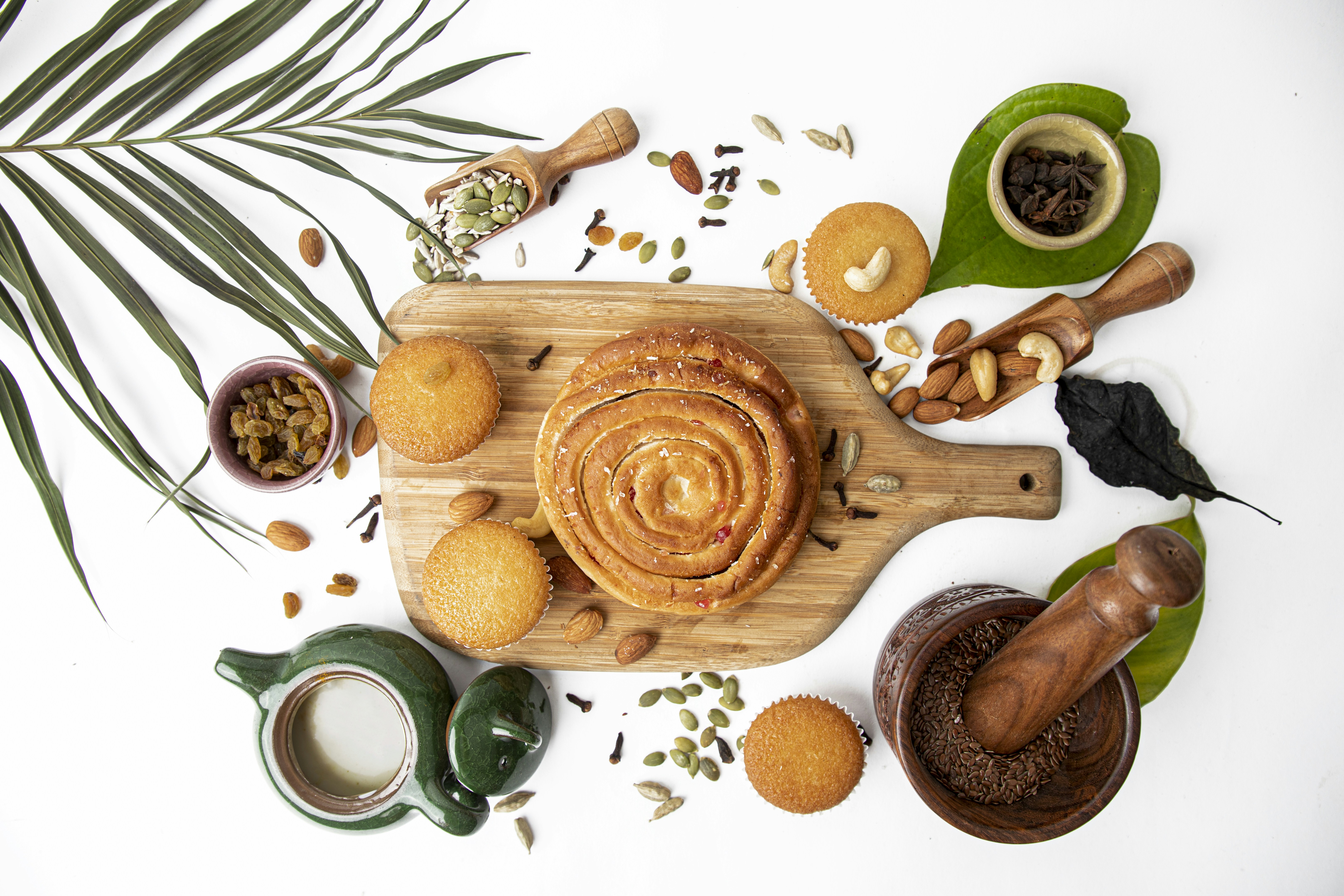 A wooden cutting board showcases a spiral pastry surrounded by an assortment of nuts, spices, and baked goods, creating a rich tapestry of textures and colors.