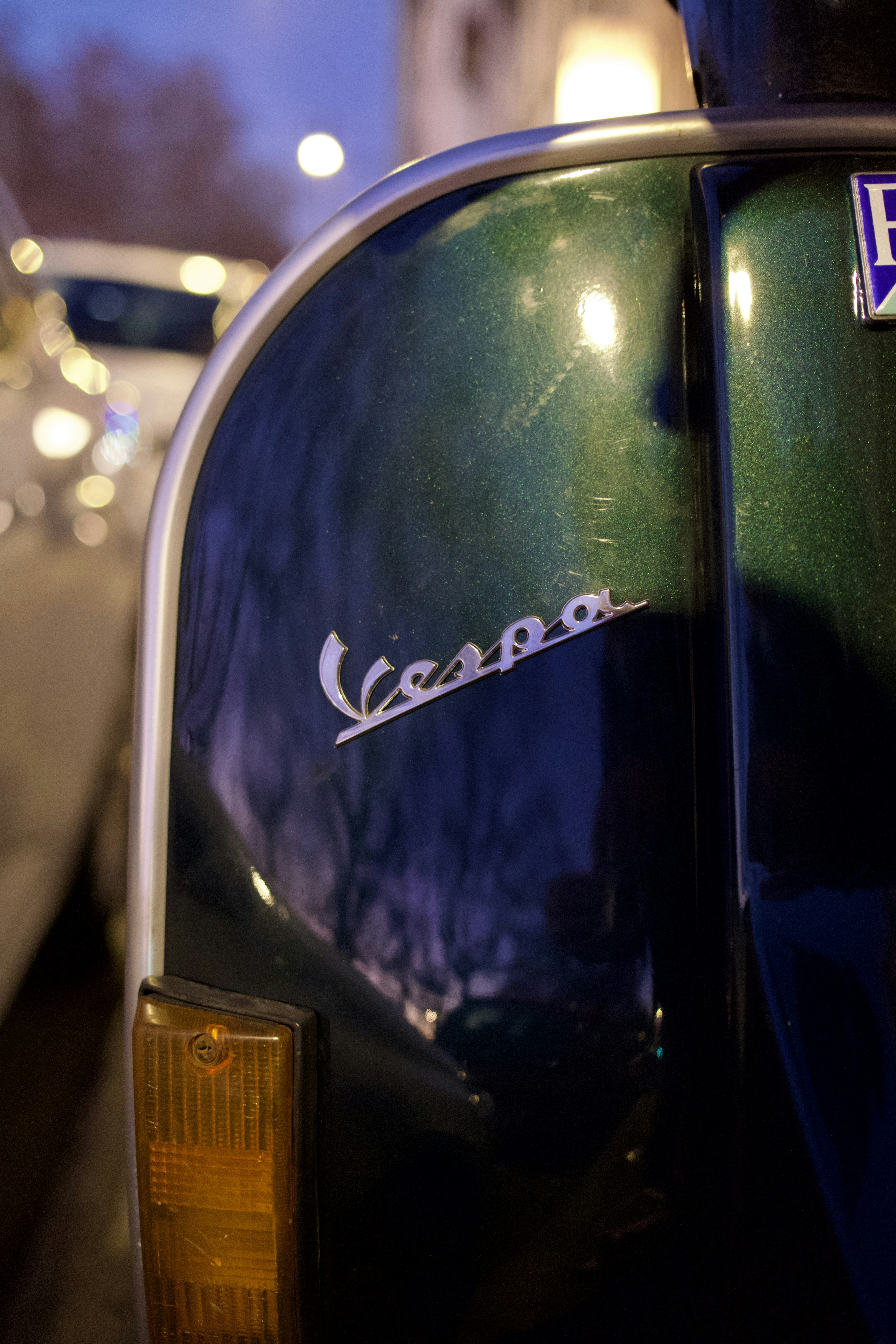 Vespa Script in Neon Quiet: A Close-Up of Chrome on Dusk-Blue Metal