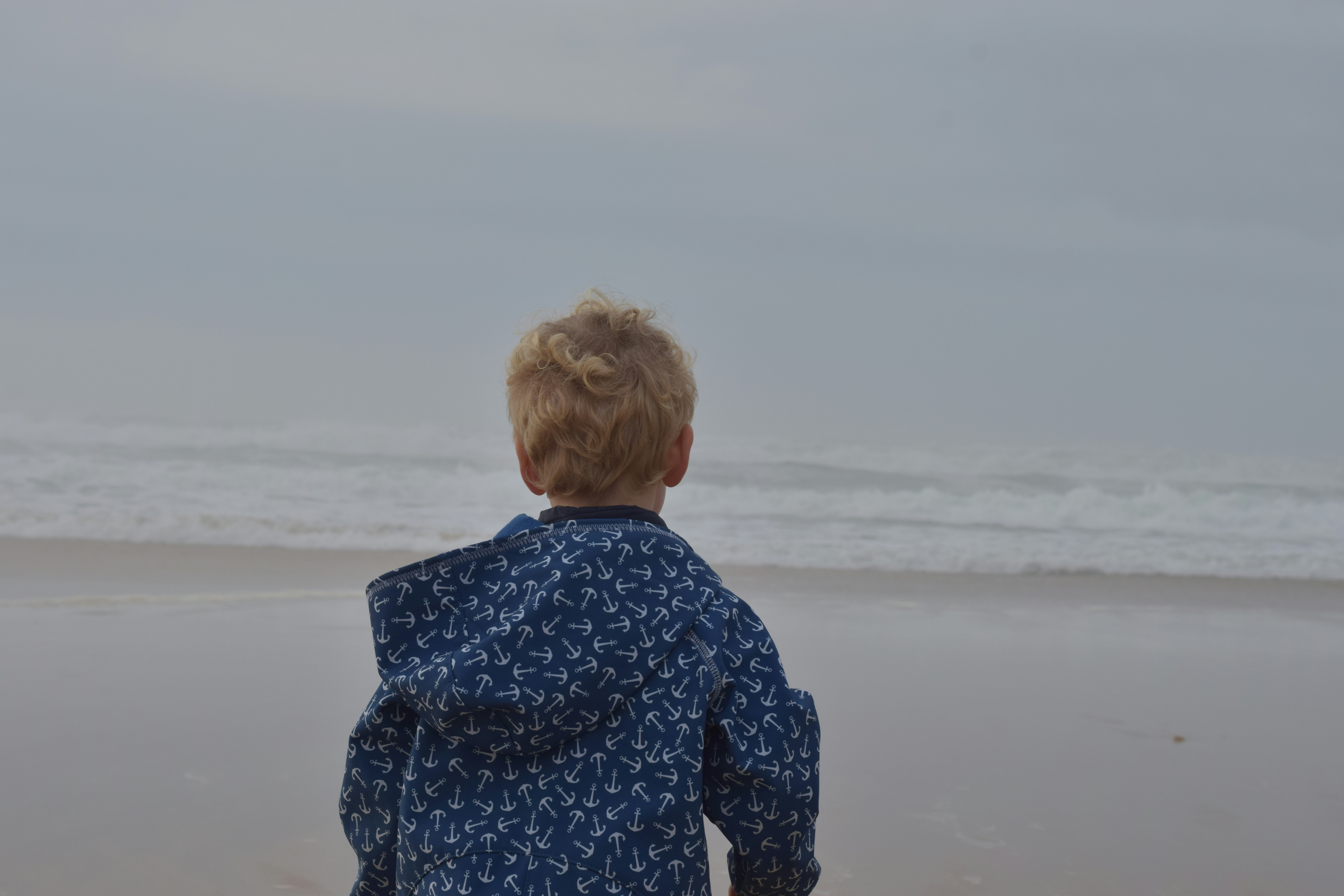Coastal Quiet: Back of a Child in a Blue Patterned Jacket Gazes Toward the Sea