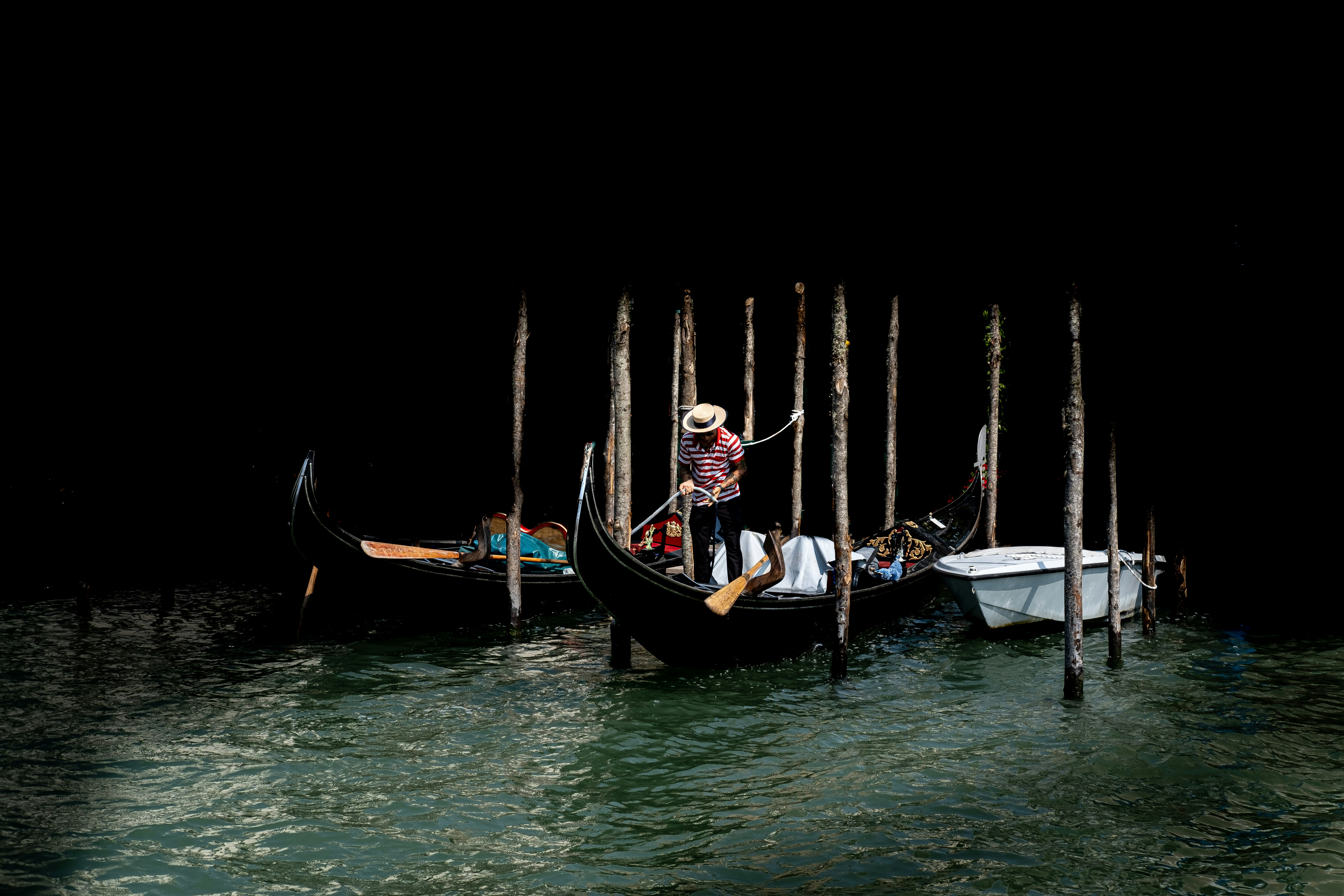 Gondolier navigating through still waters surrounded by wooden poles, creating a serene atmosphere in a darkened setting.