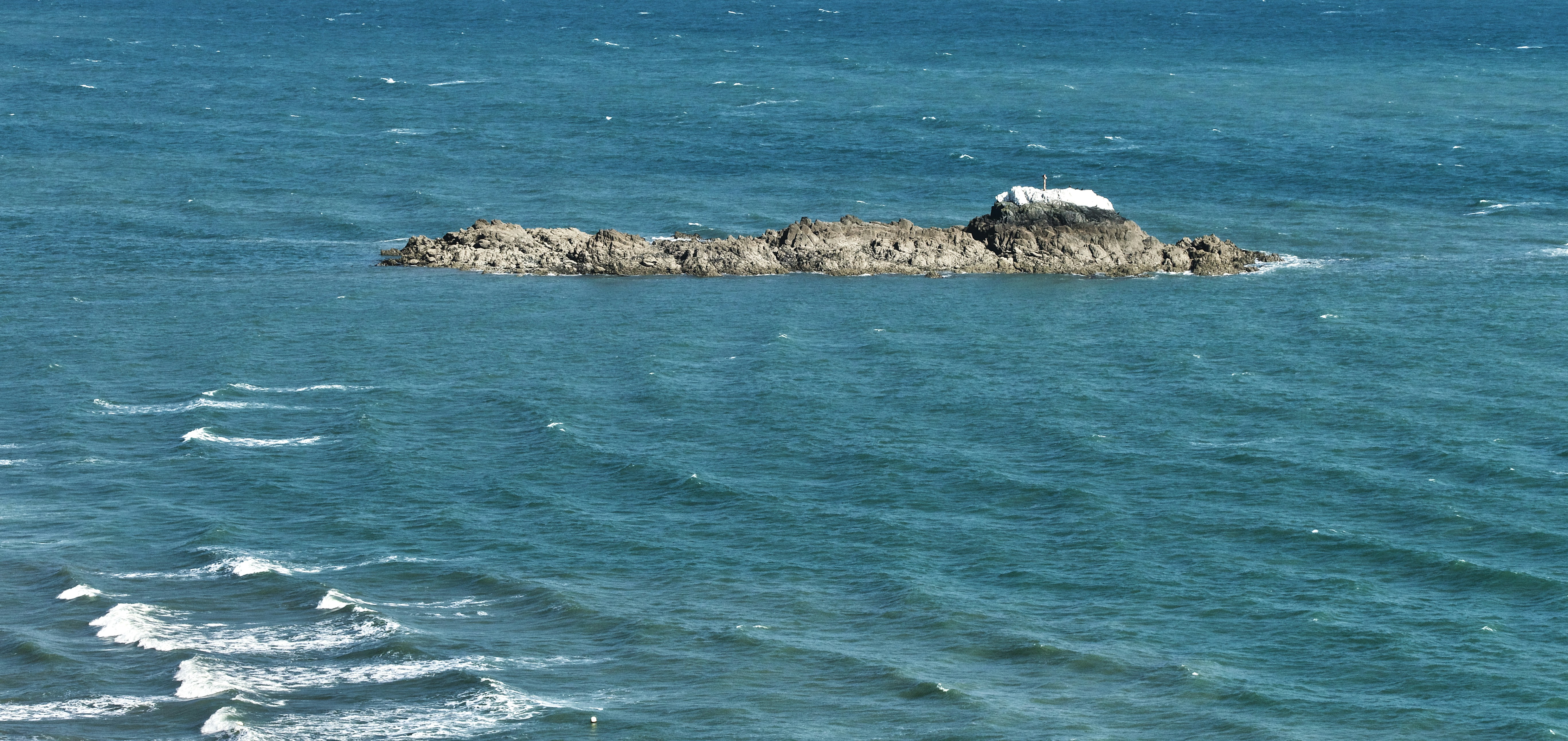 Rocky outcrop surrounded by gentle waves in a tranquil sea, highlighting nature's solitude.