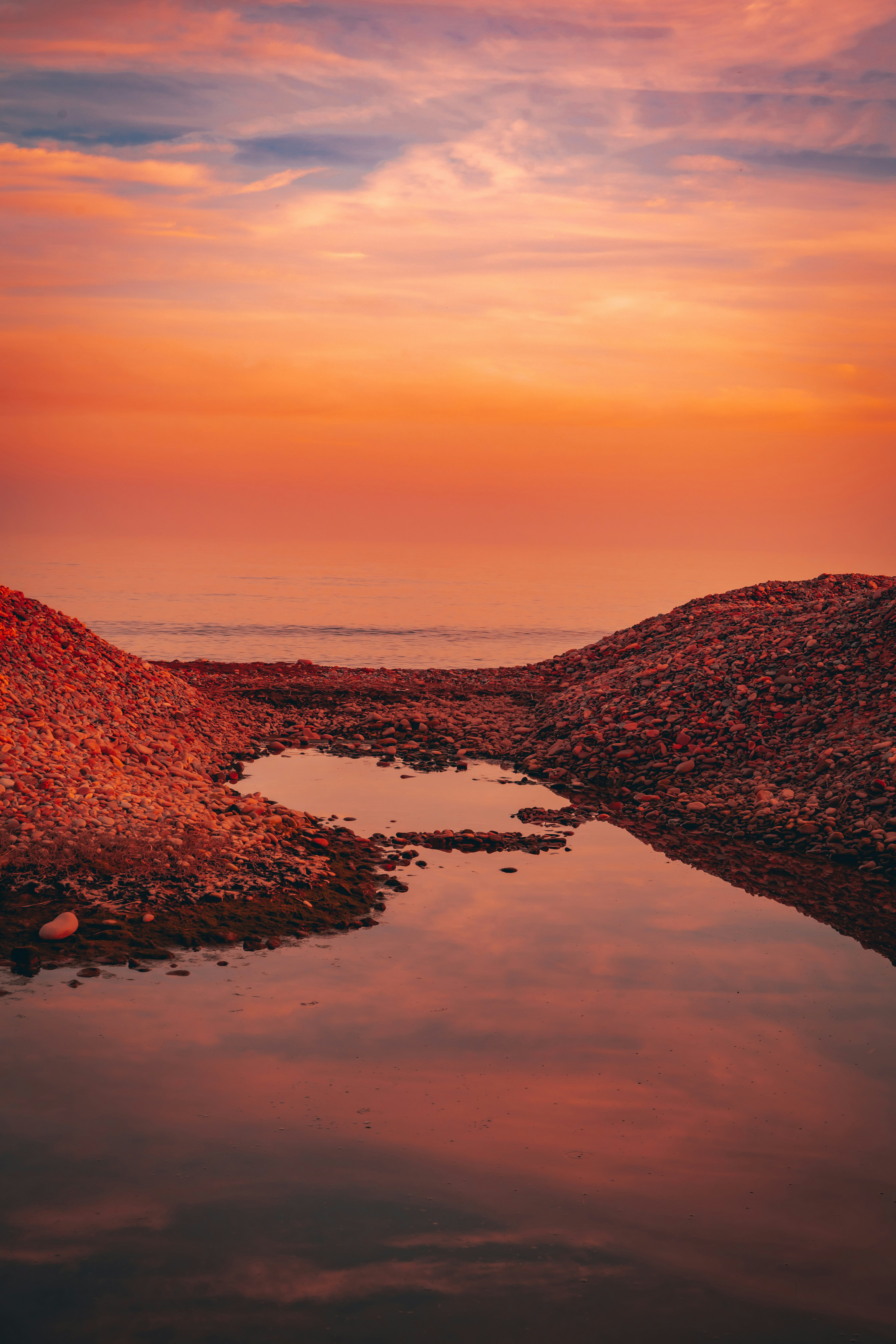 Sunset hues reflect in a small water pool surrounded by rocky mounds.