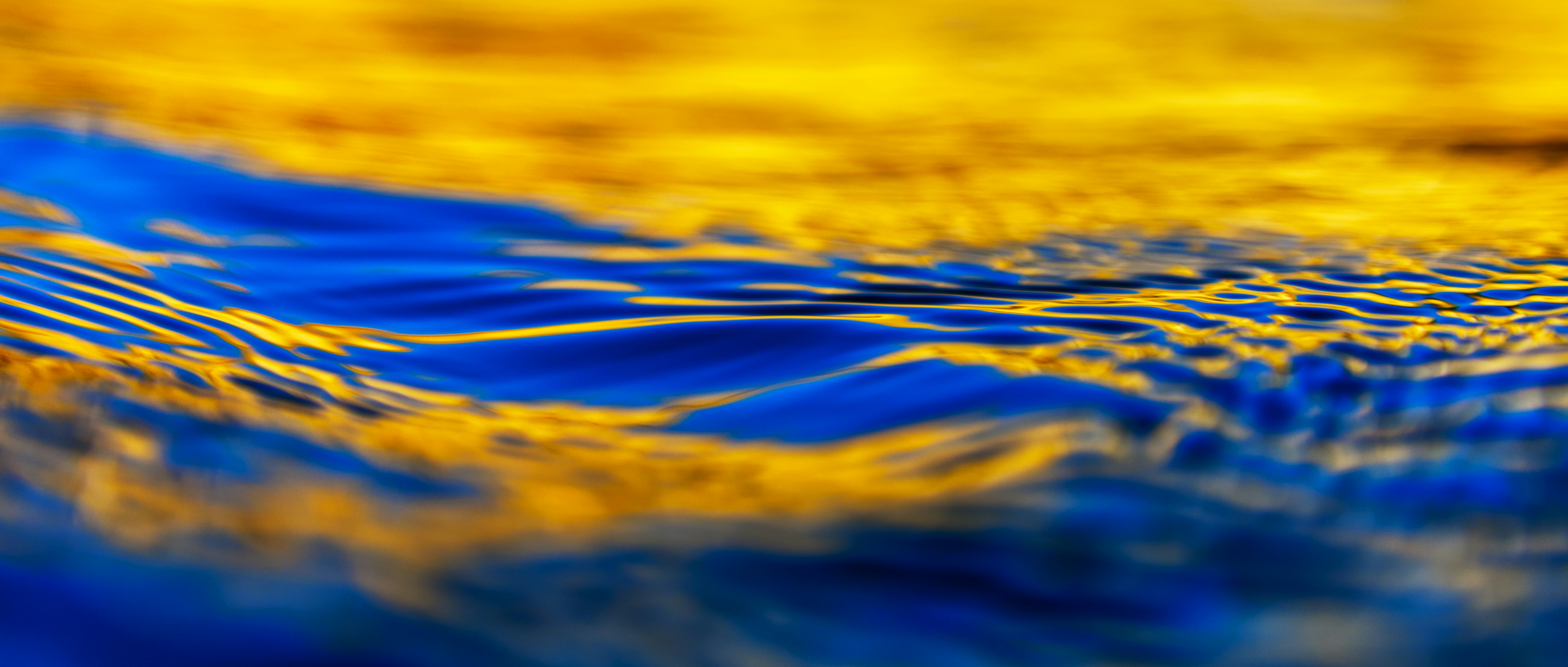 Rippling water reflects vibrant hues of blue and gold, creating a mesmerizing abstract pattern. The interplay of colors evokes a sense of tranquility.