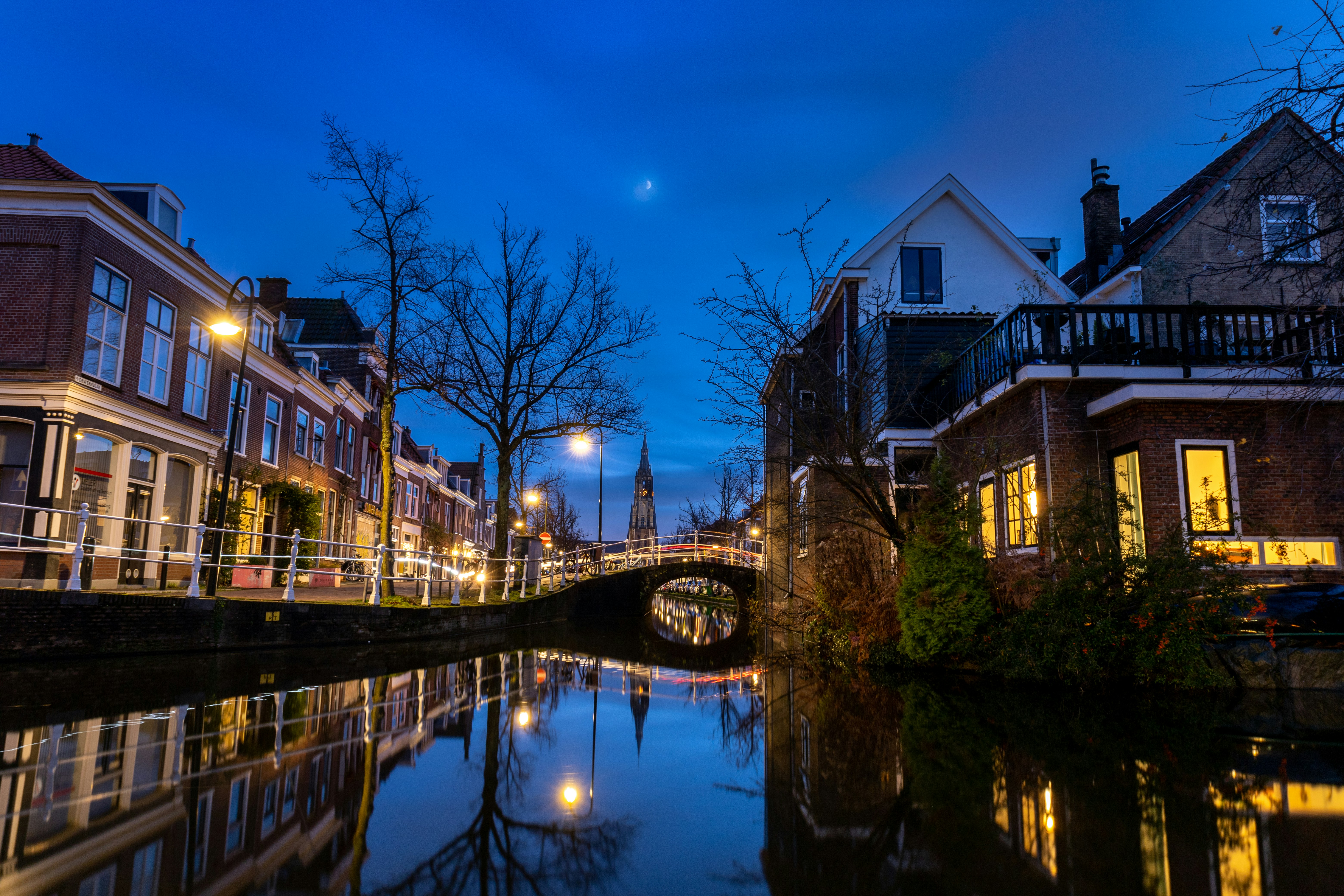 Quaint city canal with a bridge and illuminated buildings under a twilight sky.