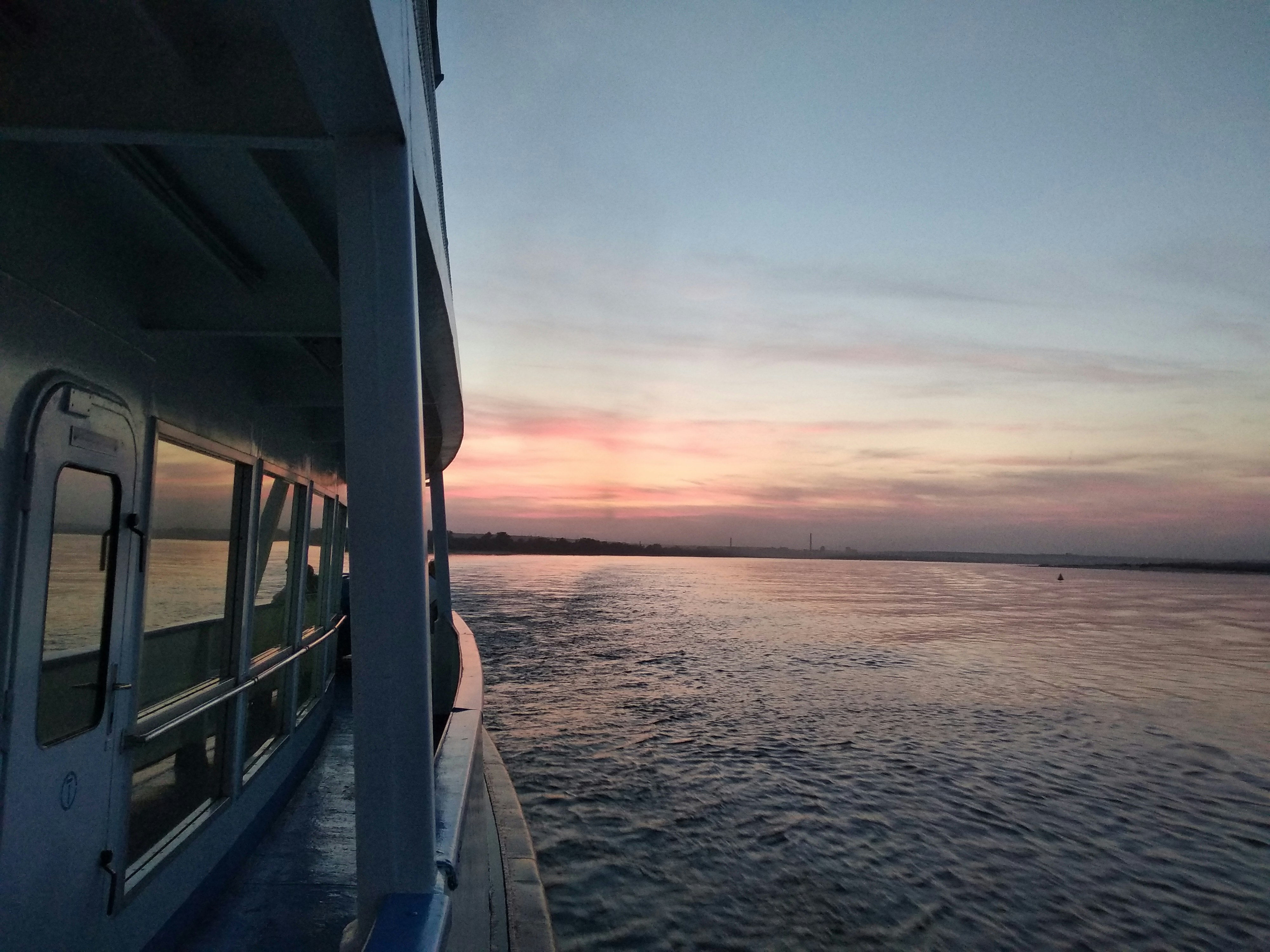 Ship deck view at sunset with calm waters and a vibrant sky.