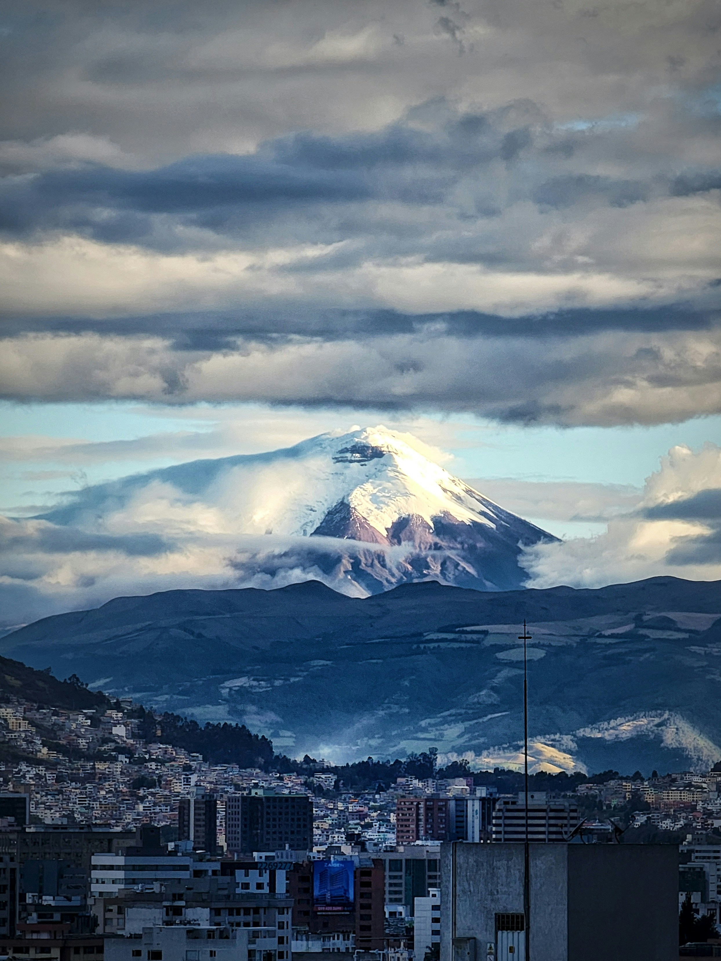 Volcan Cotopaxi from Quito,  Ecuador  | a large snow covered mountain towering over a city