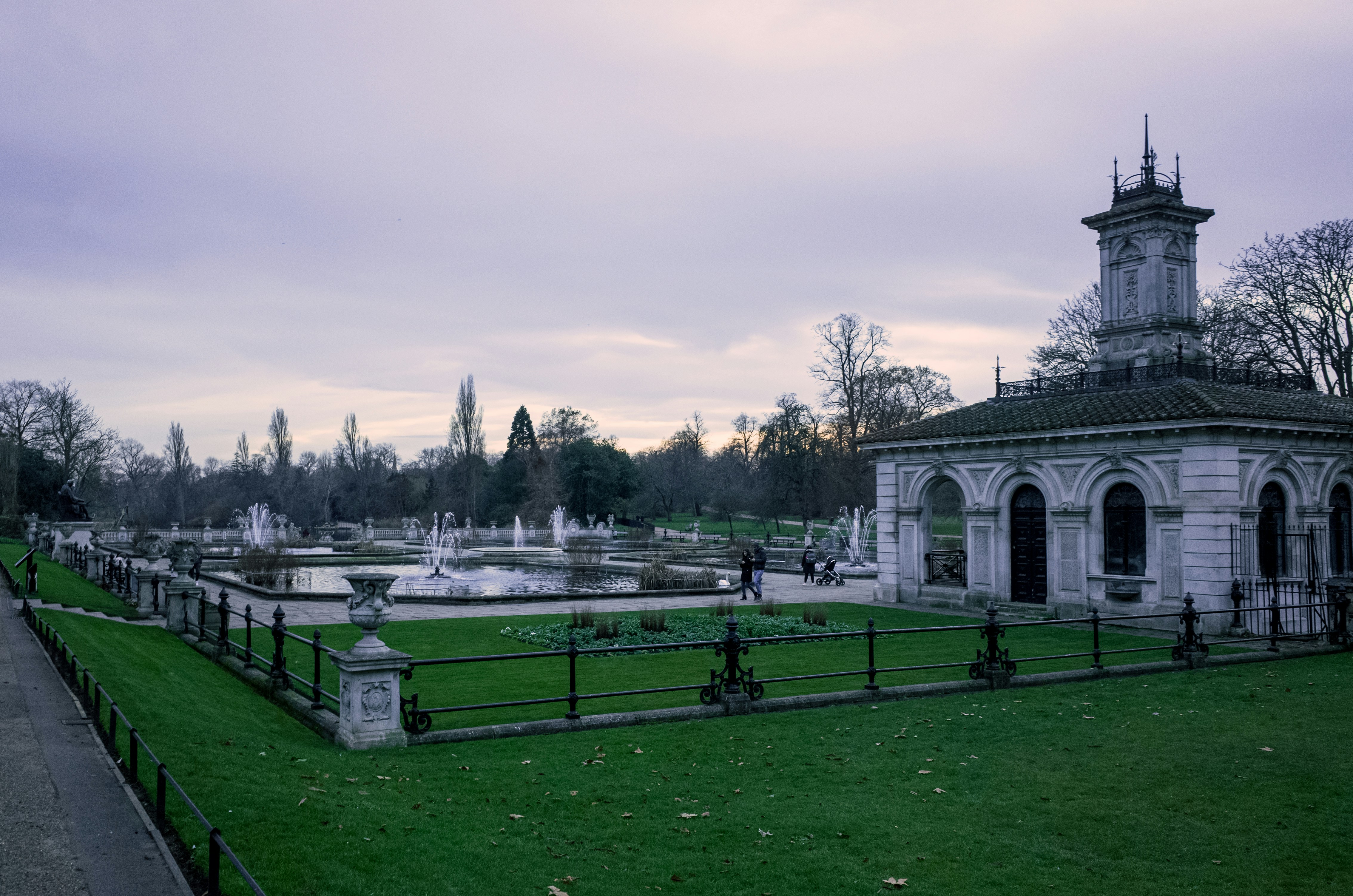 Elegant fountain surrounded by manicured gardens and historic architecture in a tranquil park setting.