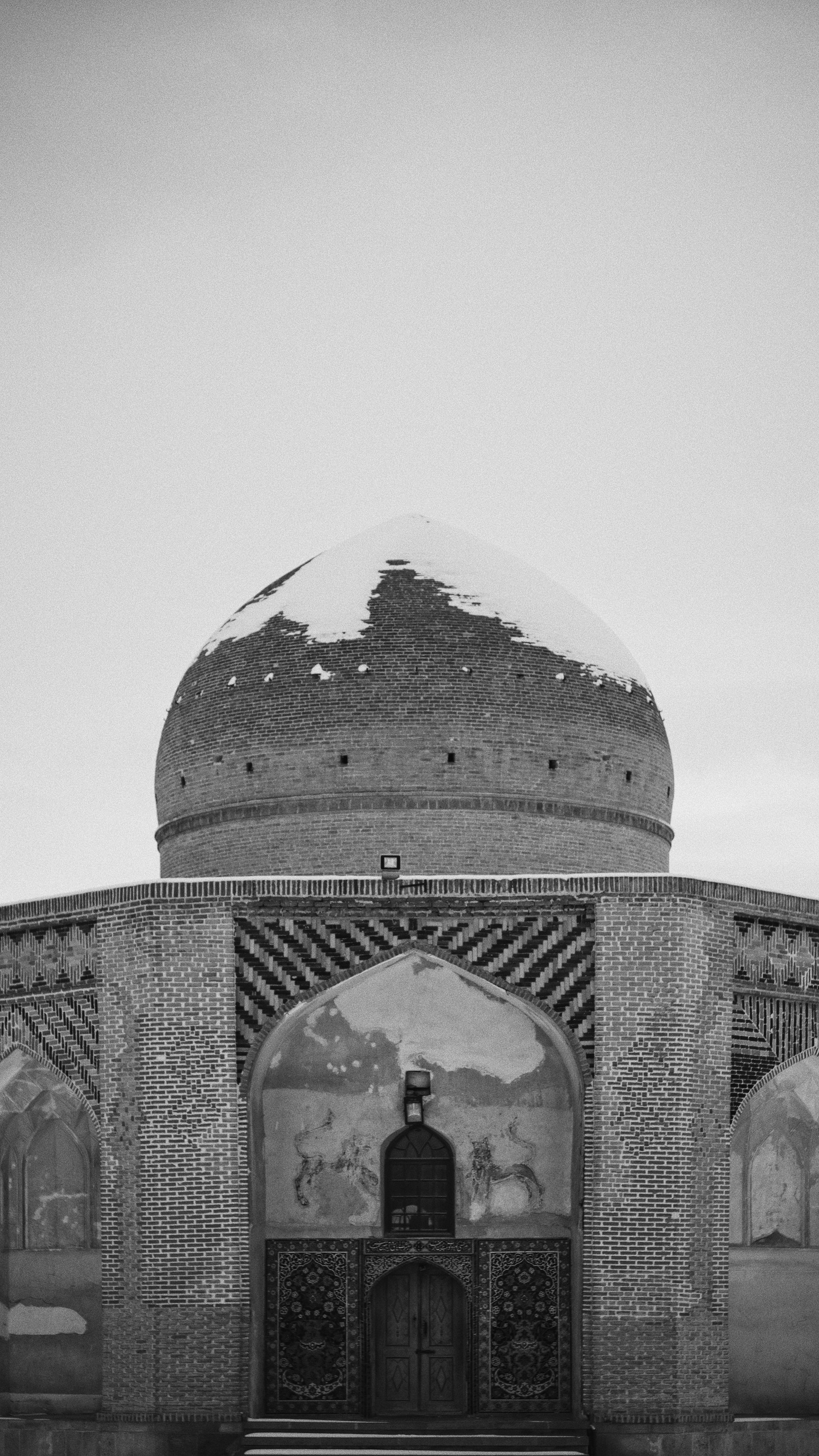 Historic dome structure adorned with intricate patterns and a dusting of snow, set against a muted sky.
