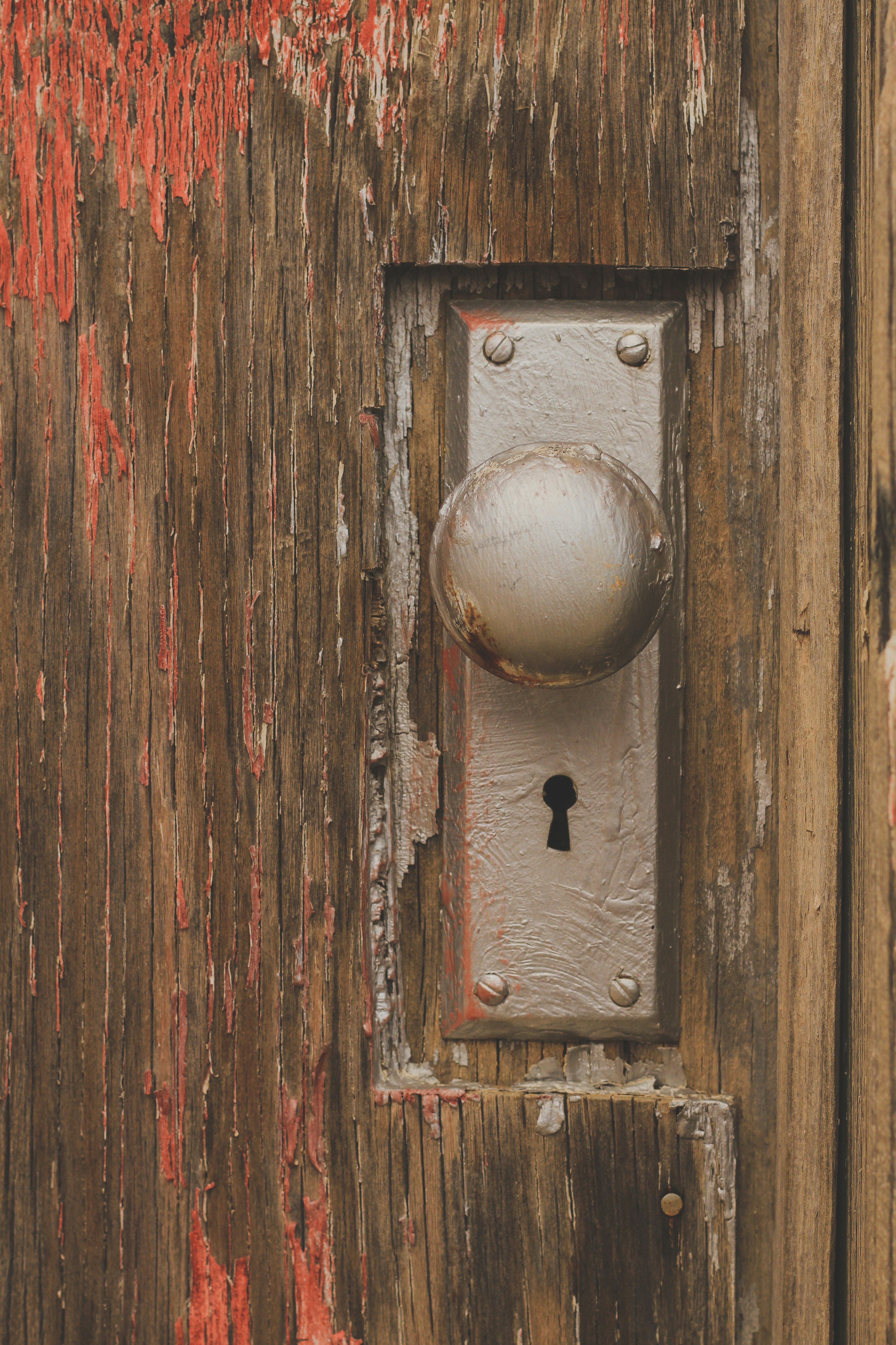 Close-up of a vintage door handle and keyhole on weathered wood, showcasing layers of peeling paint and texture.