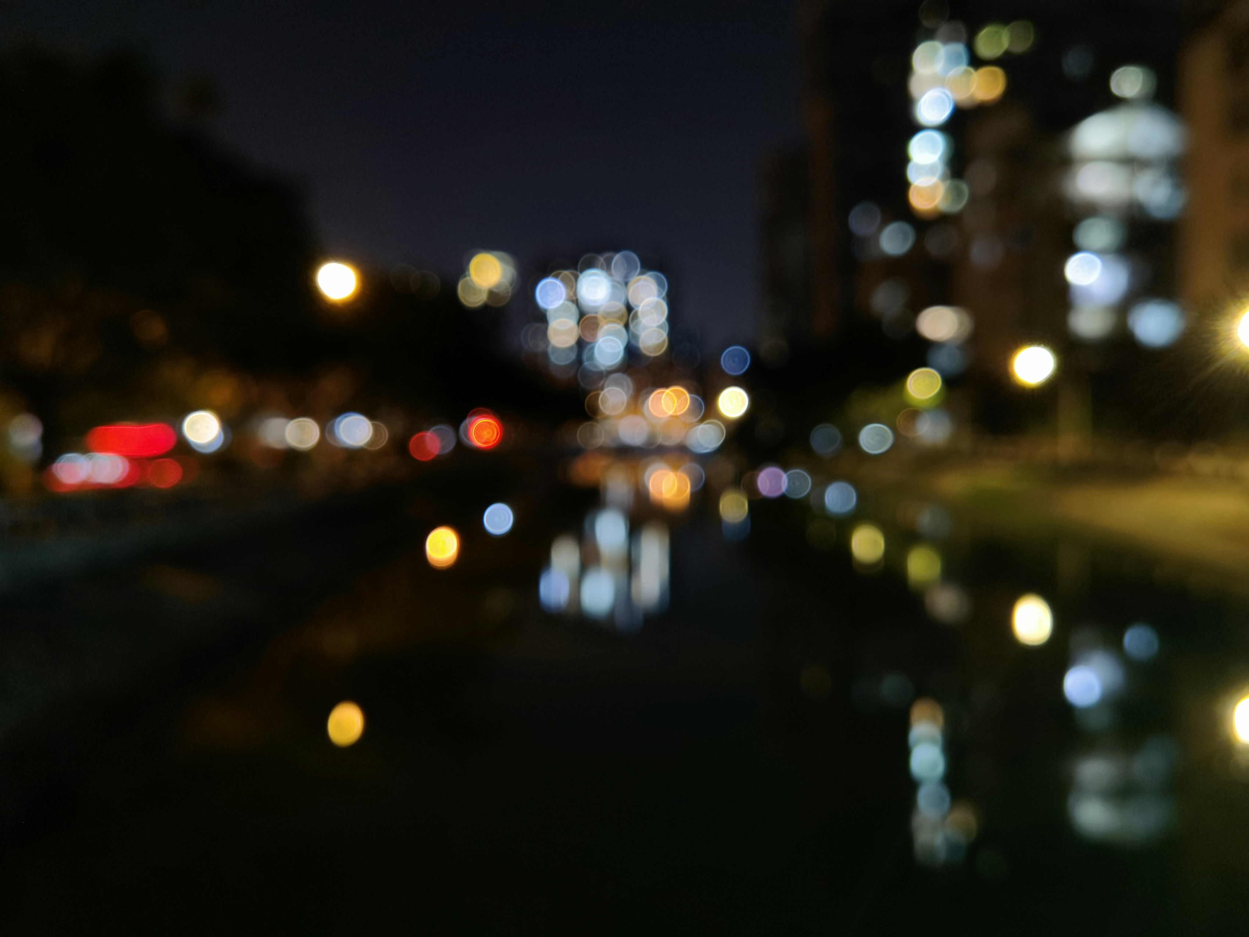 A blurred view of a city canal at night, with colorful bokeh from lights reflecting on the water's surface.