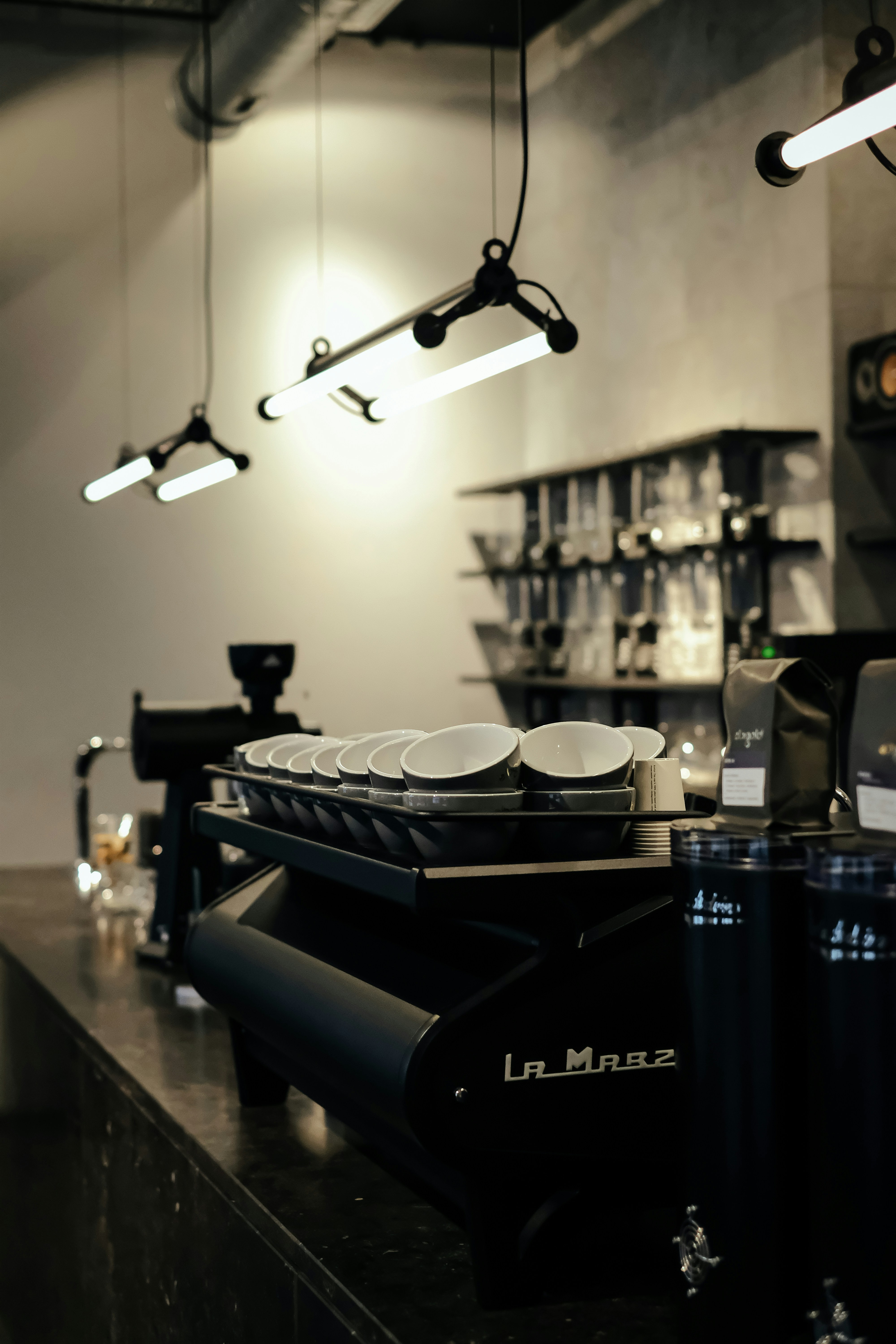 Sleek coffee machine with stacked cups in a modern café setting, highlighted by minimalist lighting.