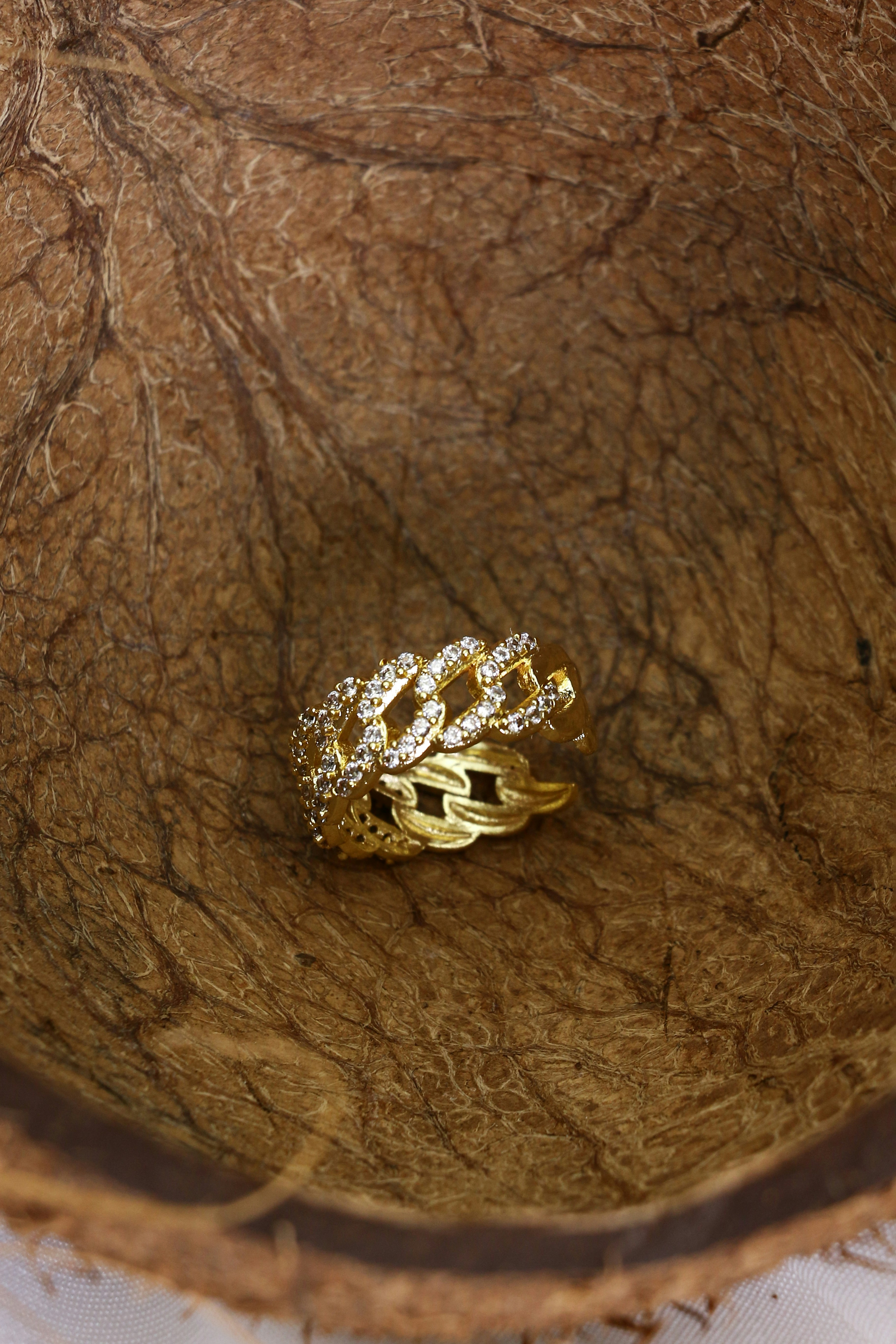 Intricately designed golden ring adorned with sparkling stones, resting inside a textured natural bowl.